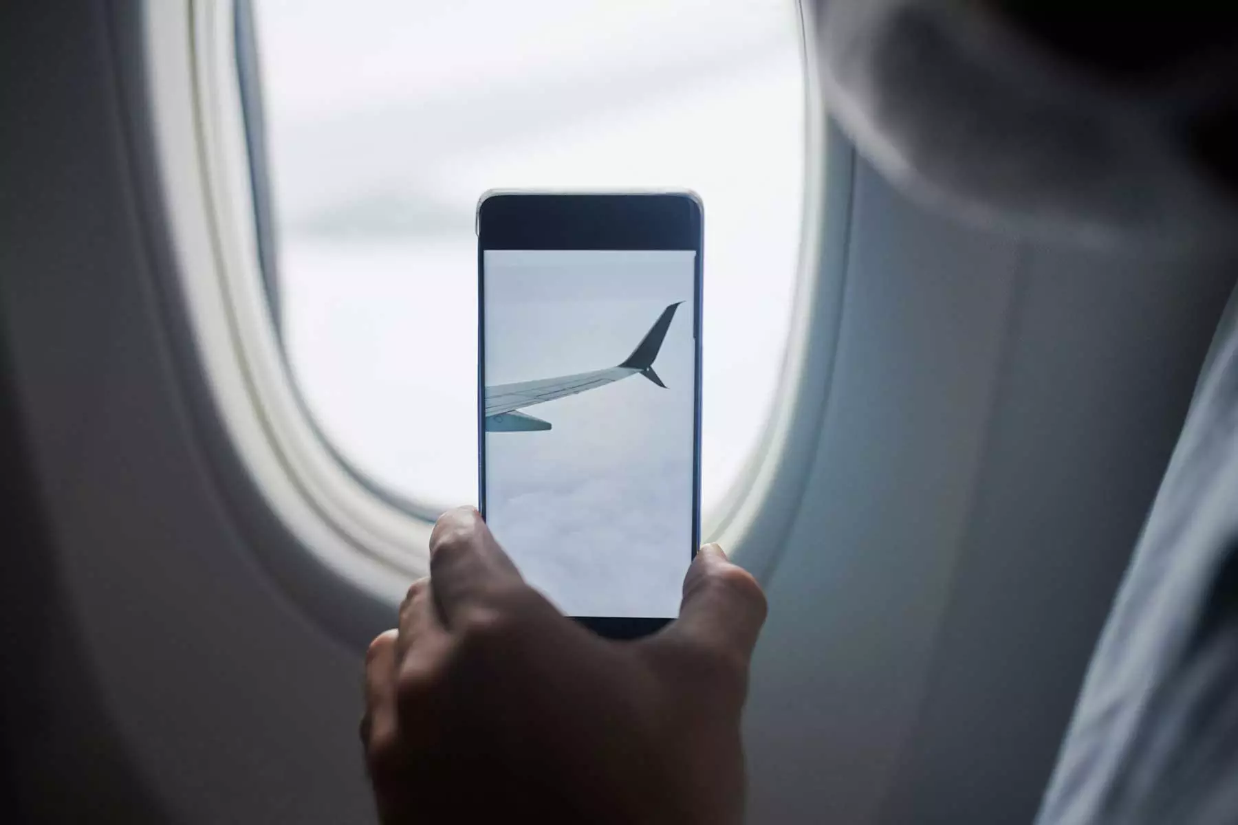 हवाईजहाजबाट दृश्यको तस्बिर लिनको लागि स्मार्टफोन प्रयोग गरेर मानिसको क्रप गरिएको शट