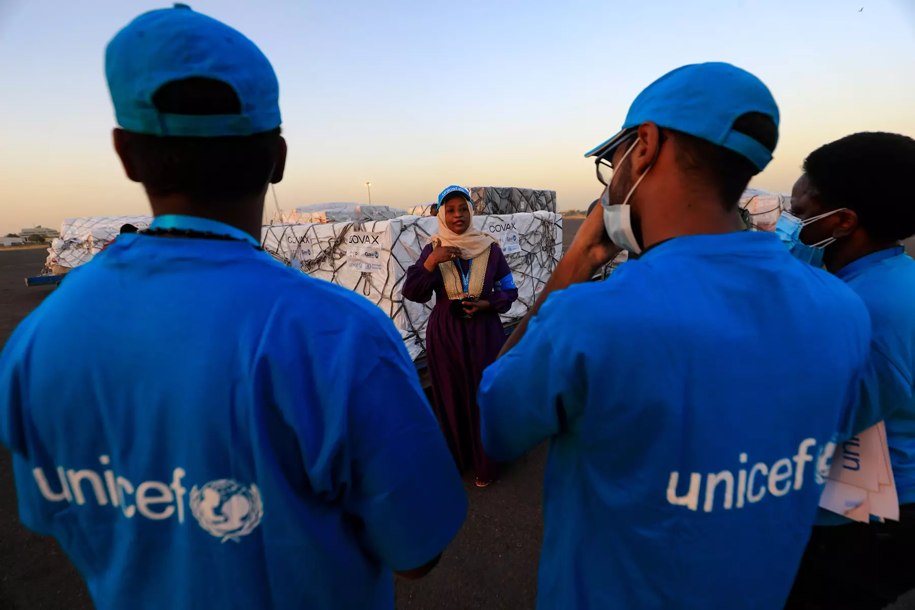 Cuirtear fostaithe Chiste Éigeandála Idirnáisiúnta Leanaí na Náisiún Aontaithe (UNICEF) ar an eolas nuair a tháinig an chéad bhaisc de vacsaíní coronavirus, ag aerfort Khartoum i bpríomhchathair na Súdáine, an 3 Márta, 2121.