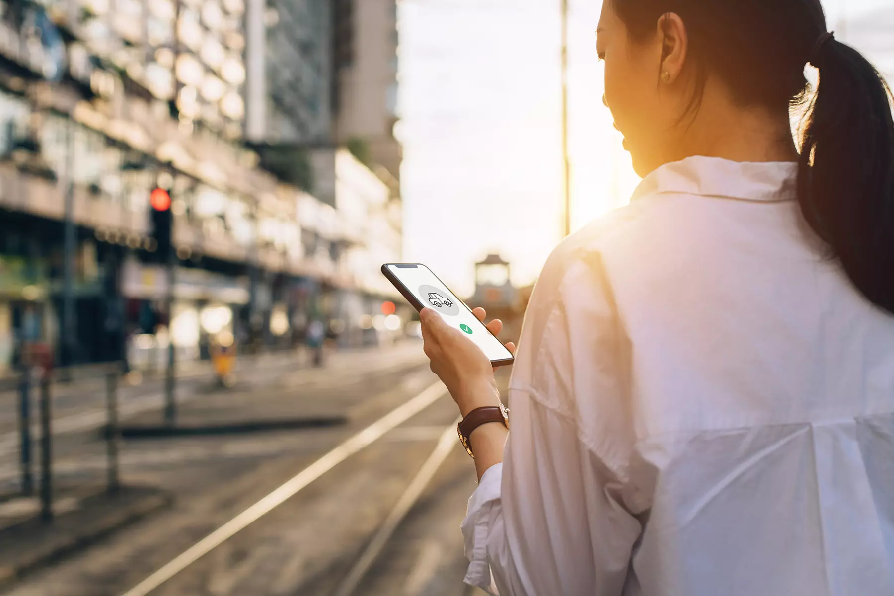 Wanita muda menggunakan aplikasi seluler di smartphone untuk mengatur perjalanan transportasi di jalan kota saat matahari terbenam