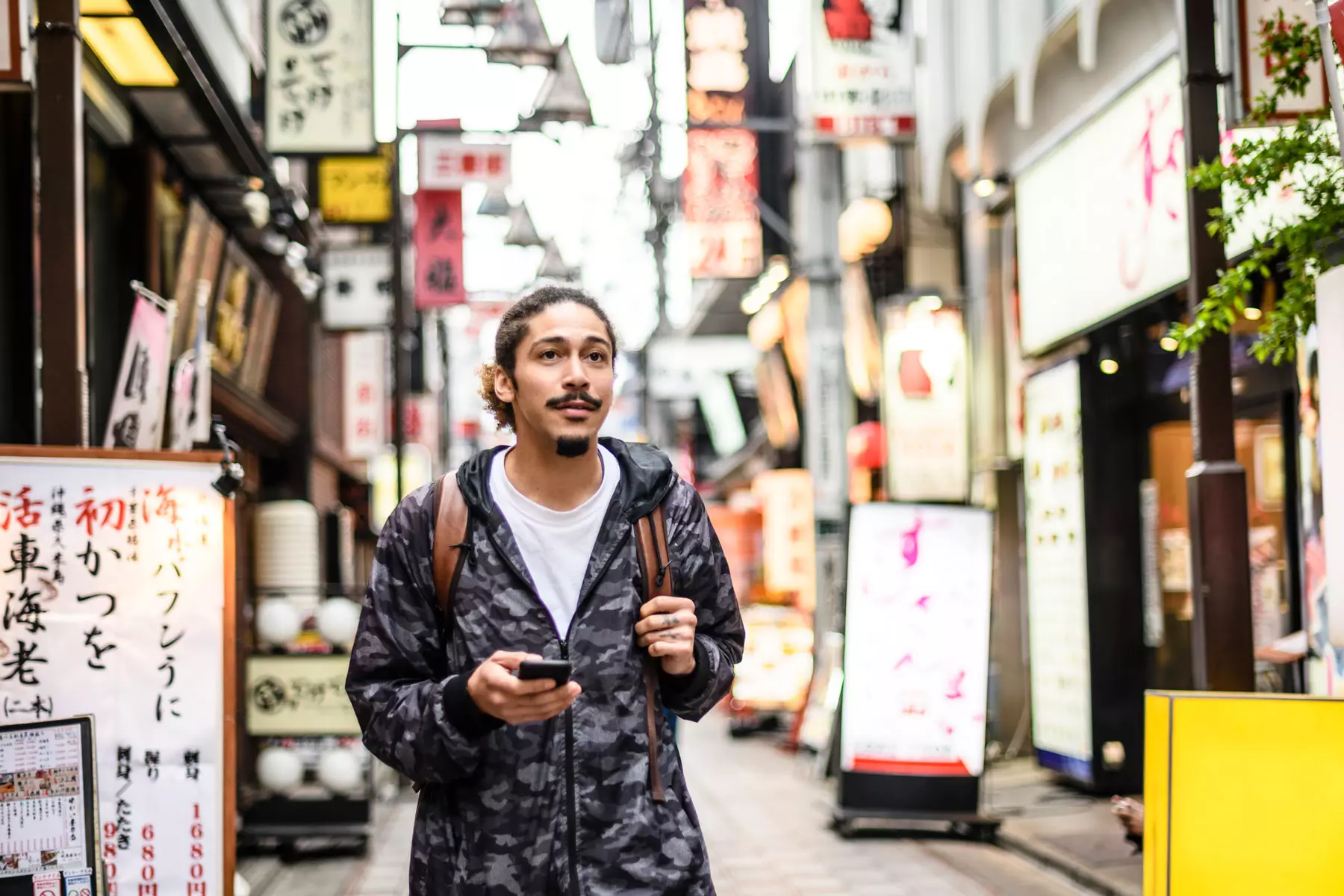 Lalaking manlalakbay na nasa edad 20 na may hawak na mobile phone at may dalang backpack sa Japan