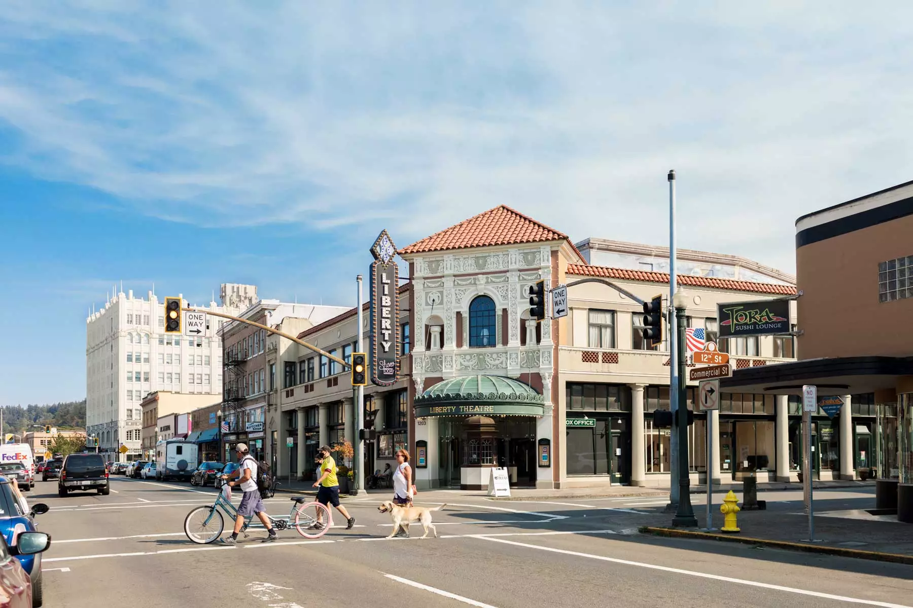 Pessoas, bicicletas e um cachorro atravessam um cruzamento no centro de Astoria, Oregon