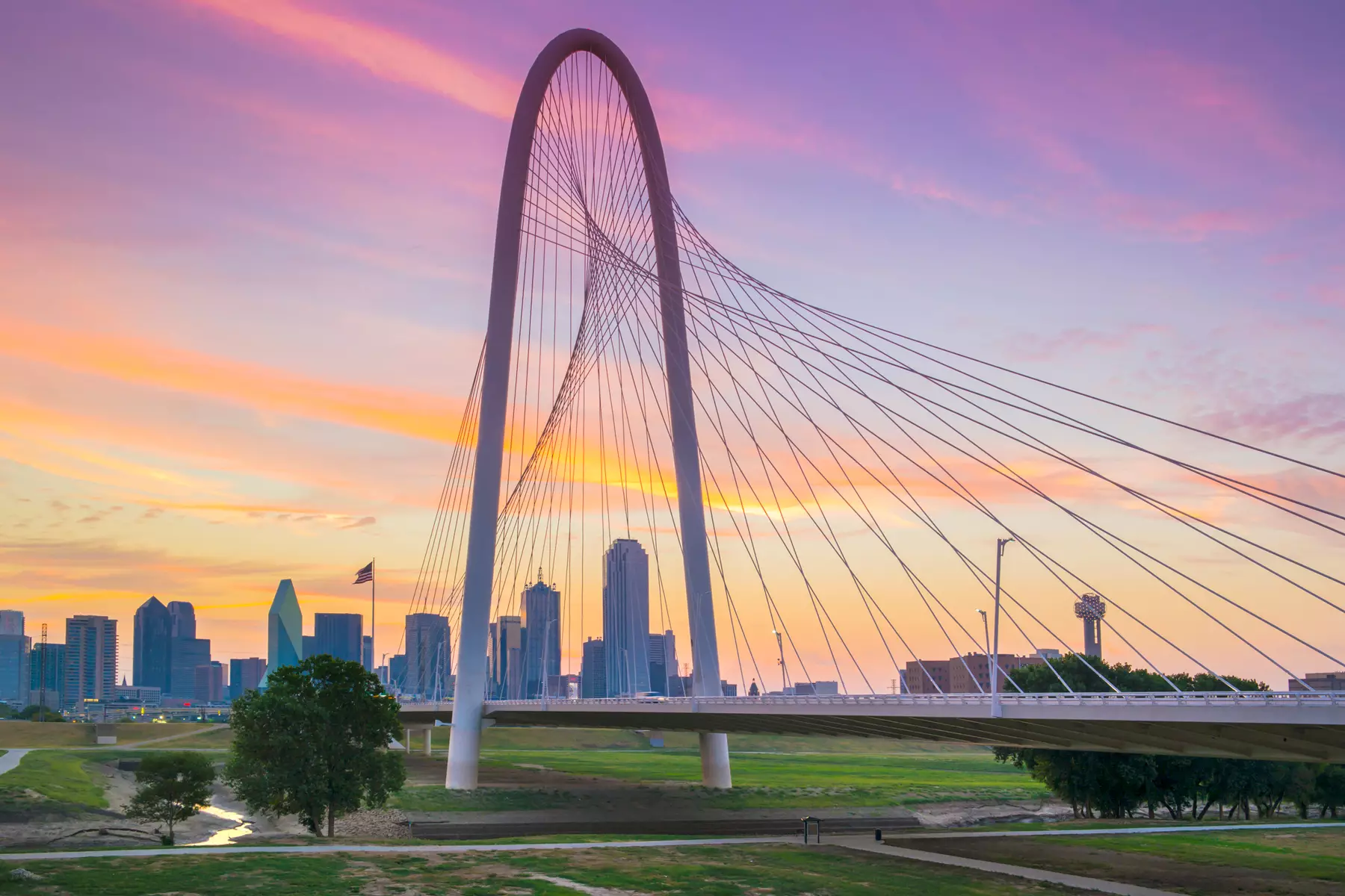 Margaret Hunt Hill Bridge kun Downtown Dallas-silueto ĉe sunleviĝo en Dallas, Teksaso.