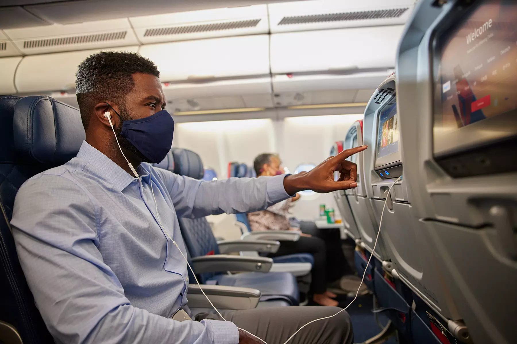 Een man met een masker scrolt door de selecties van Delta Studio op de IFE