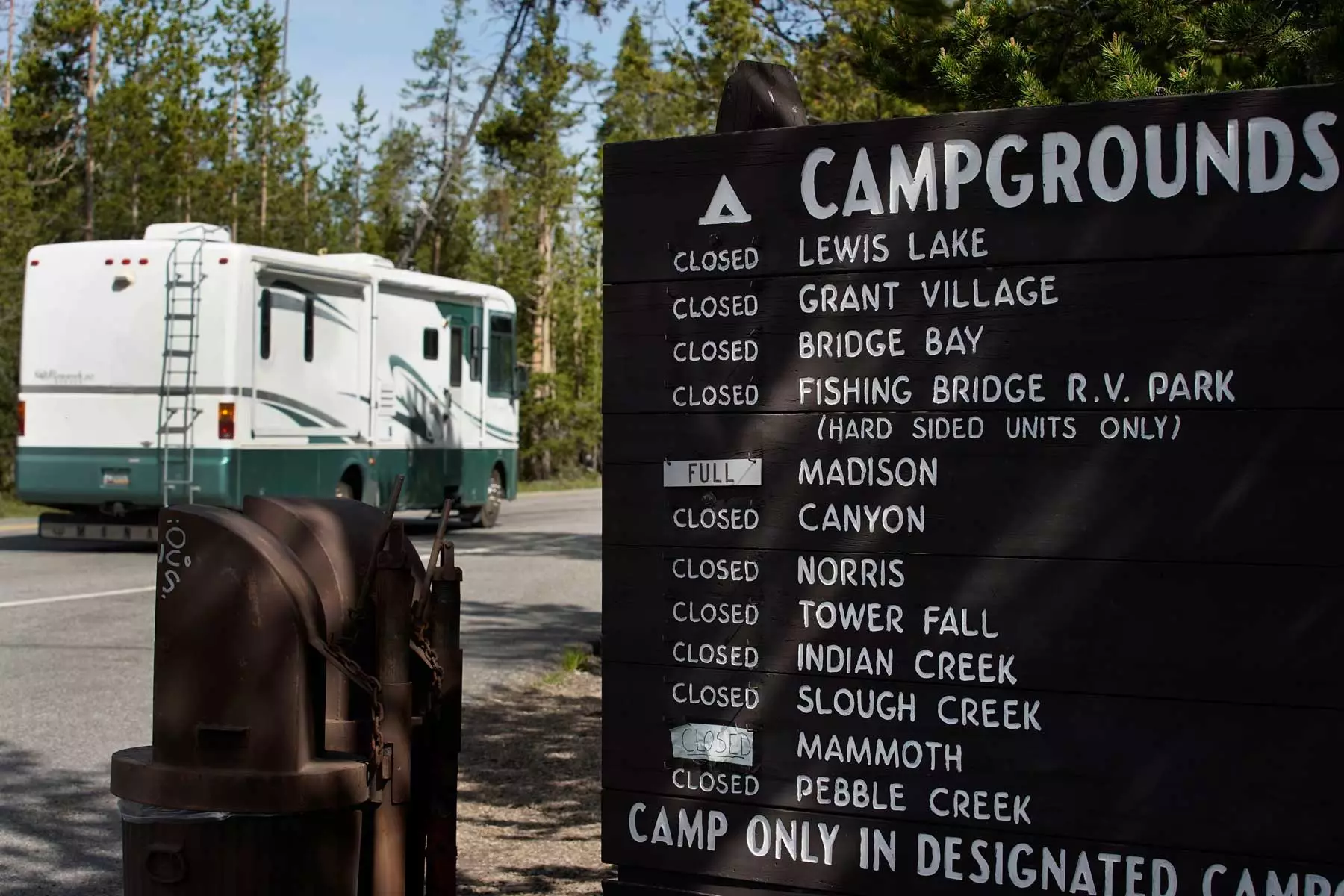 Um trailer de trailer passa por uma placa mostrando que todos, exceto um acampamento, estão abertos na entrada sul do Parque Nacional de Yellowstone em 15 de junho de 2020, nos arredores de Jackson Wyoming.