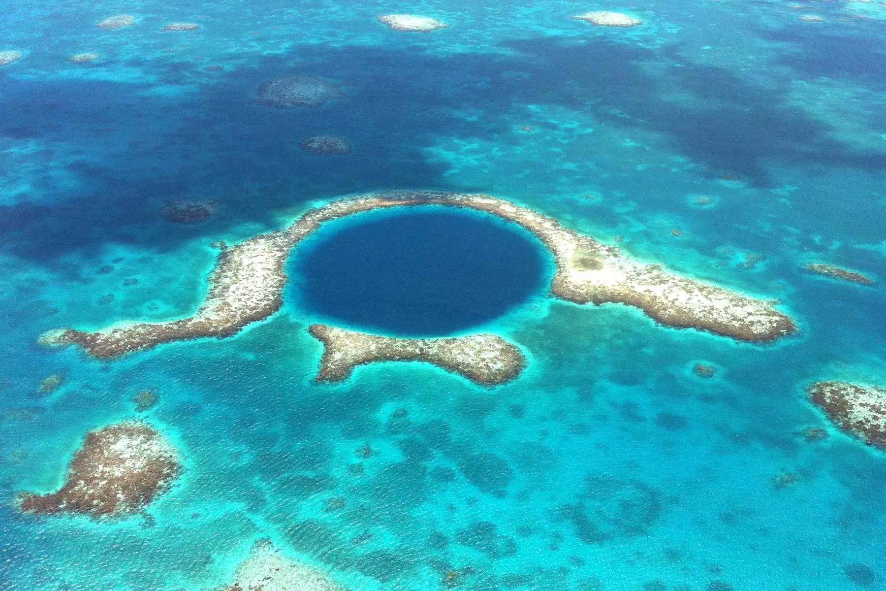 I-Great Blue Hole ngasogwini lwaseBelize ibonakala endizeni enophephela emhlane ngosuku oluhle lwasentwasahlobo.