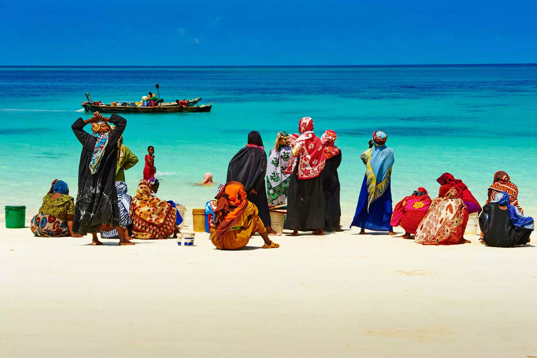 Mulleres aliñadas cun barco de pesca ao lonxe na praia de Nungwi en Unguja, illa de Zanzíbar en Tanzania. Tanzania