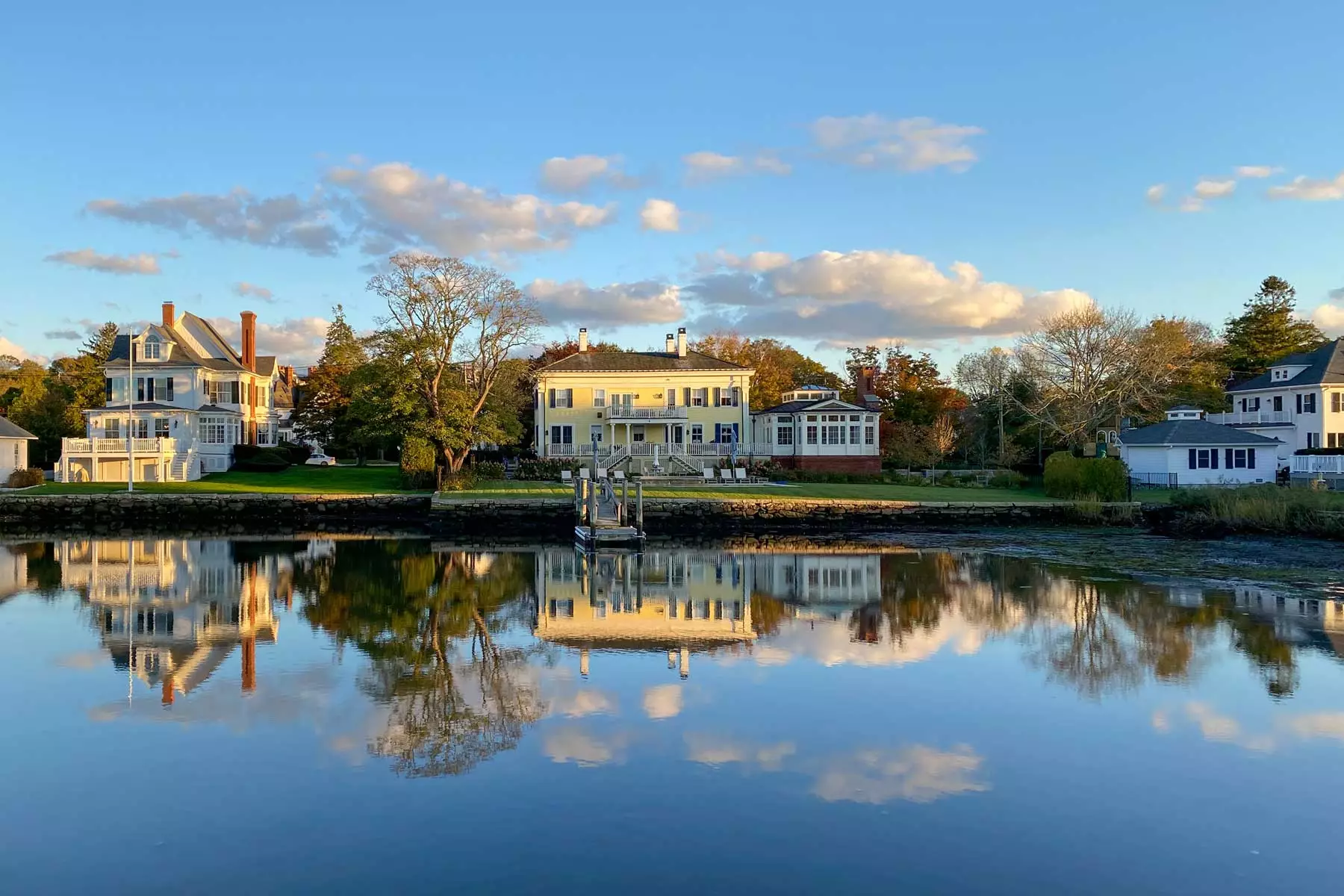 Ang pagsalop sa adlaw ubay sa Mystic River sa Mystic, Connecticut samtang ang mga pamalandong naglutaw ibabaw sa malinawon nga tubig.