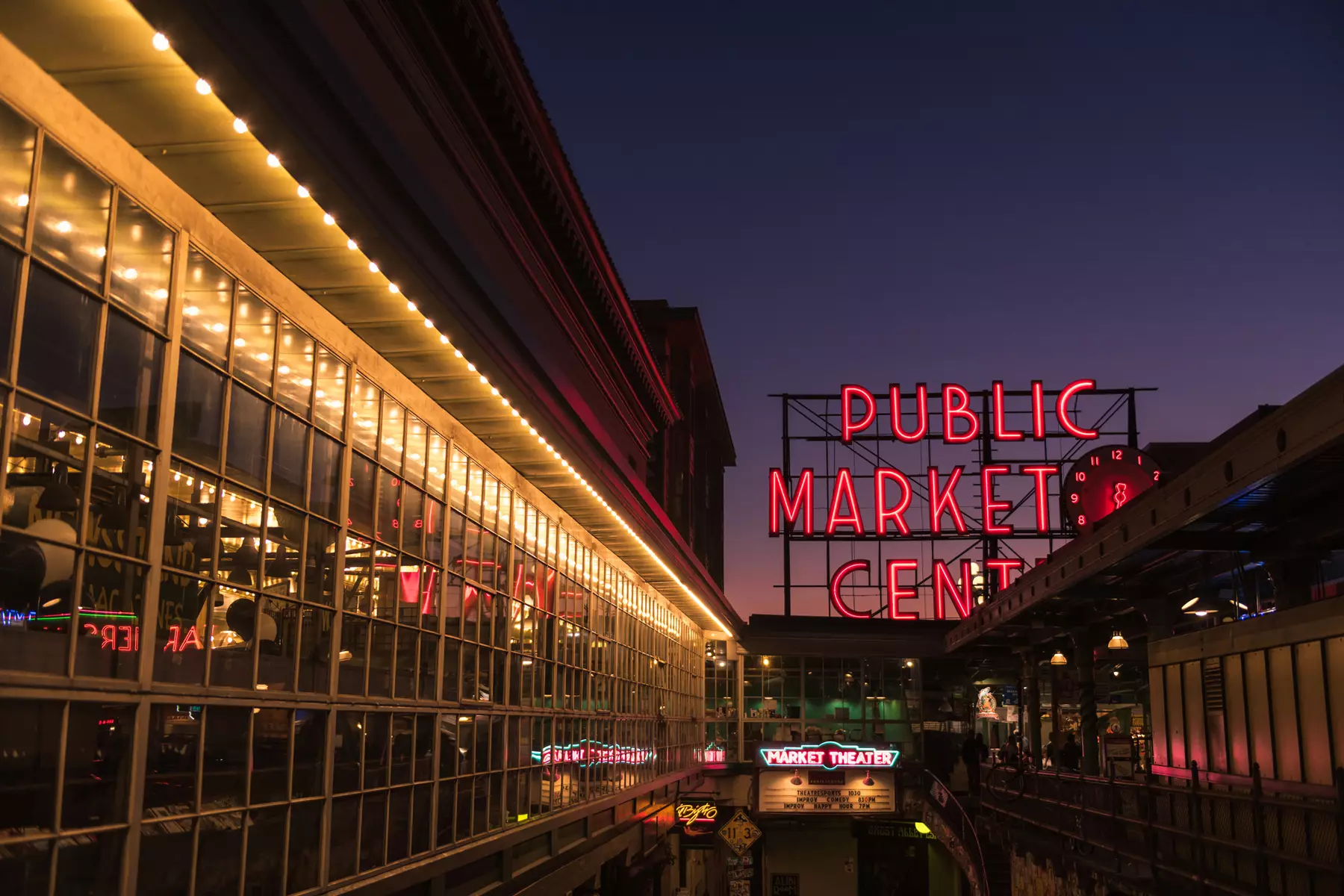 O famoso sinal de Pike Place Market iluminado ao pôr do sol sobre Post Alley.