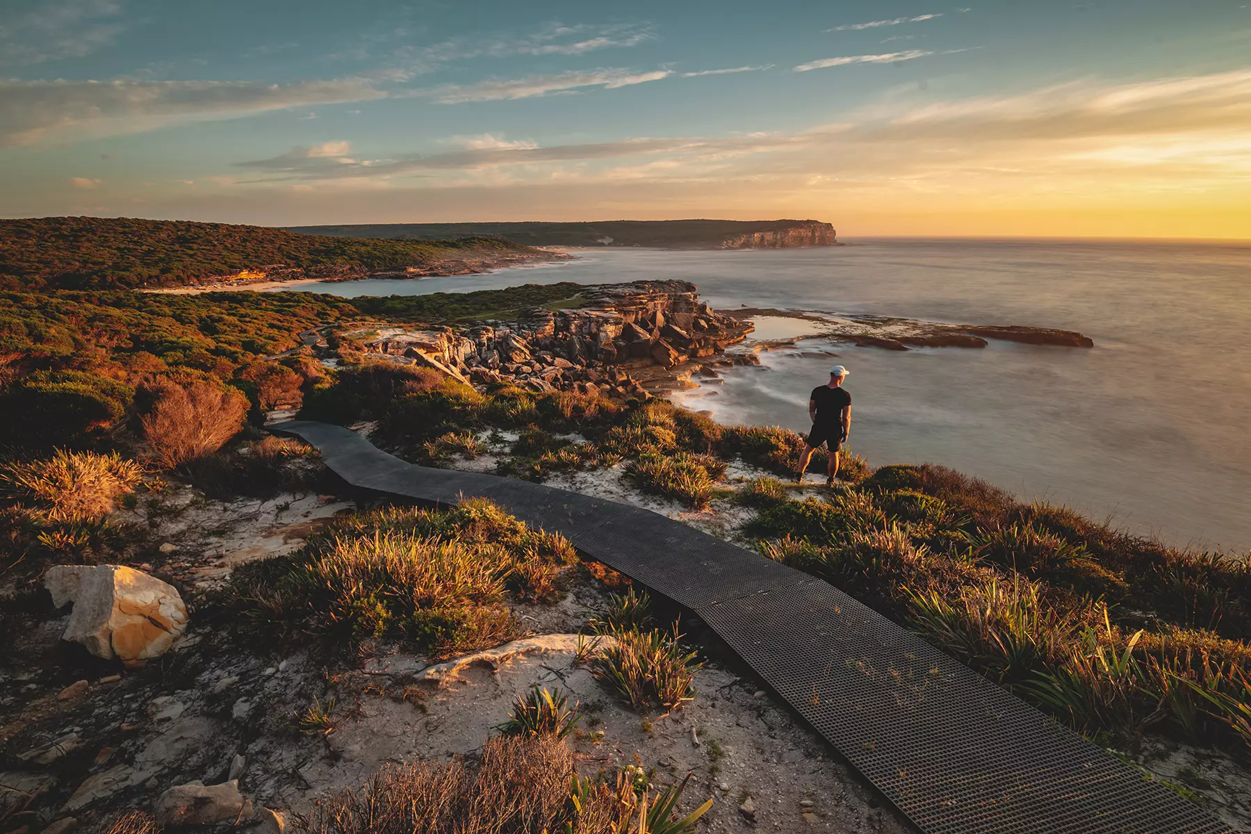 In man stie op in klif yn it Royal National Park by sinne ûndergong