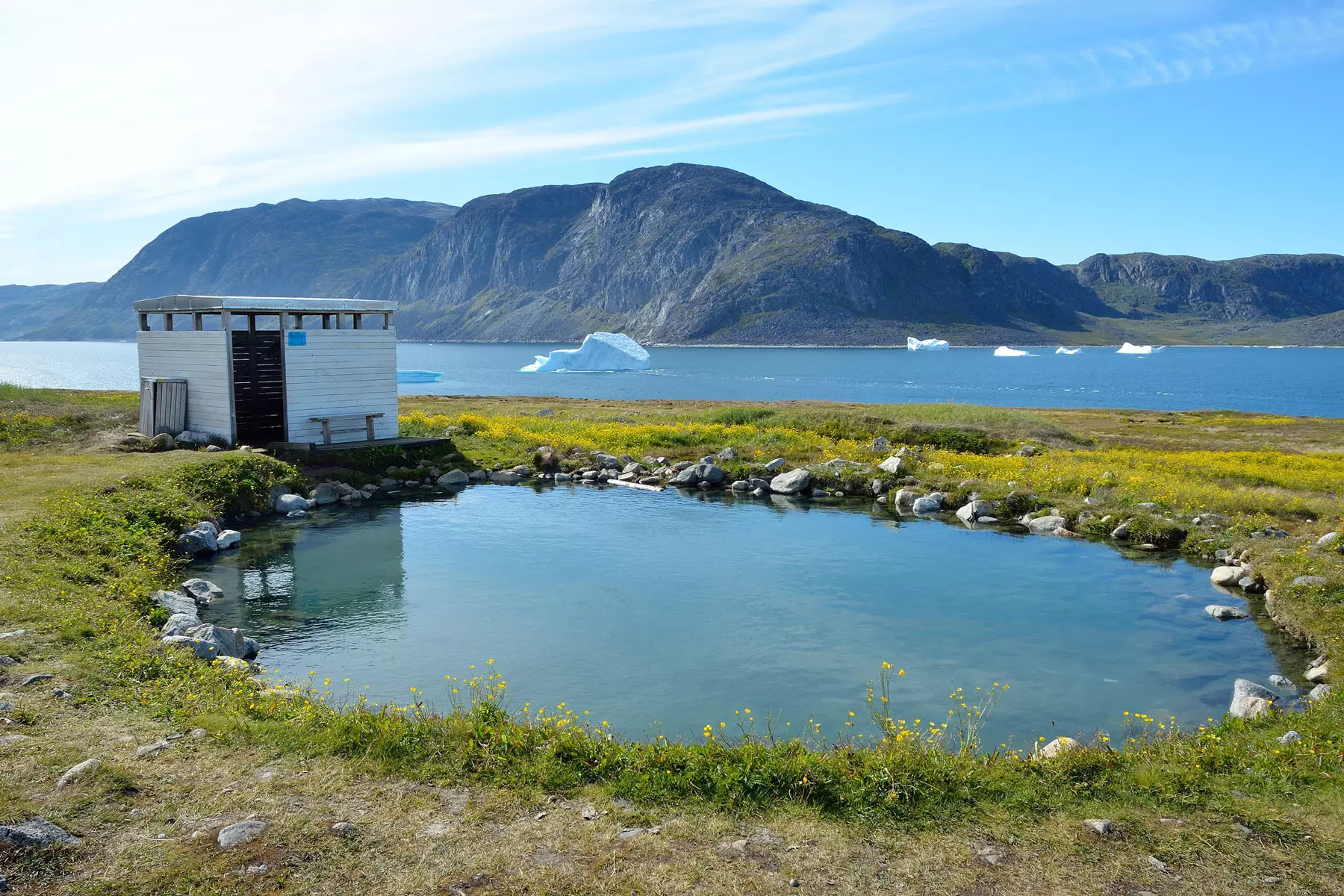 Dziwe la madzi otentha pafupi ndi nyanja ndi mapiri pa tsiku la dzuwa ku Uunartoq, Greenland