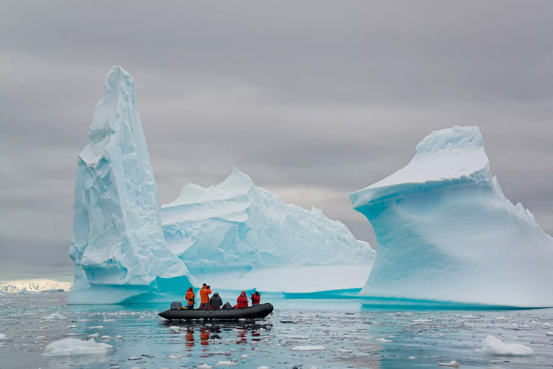 Personas en pequeños botes zodiac inflables pasando imponentes icebergs esculpidos en las tranquilas aguas alrededor de las pequeñas islas de la península antártica.