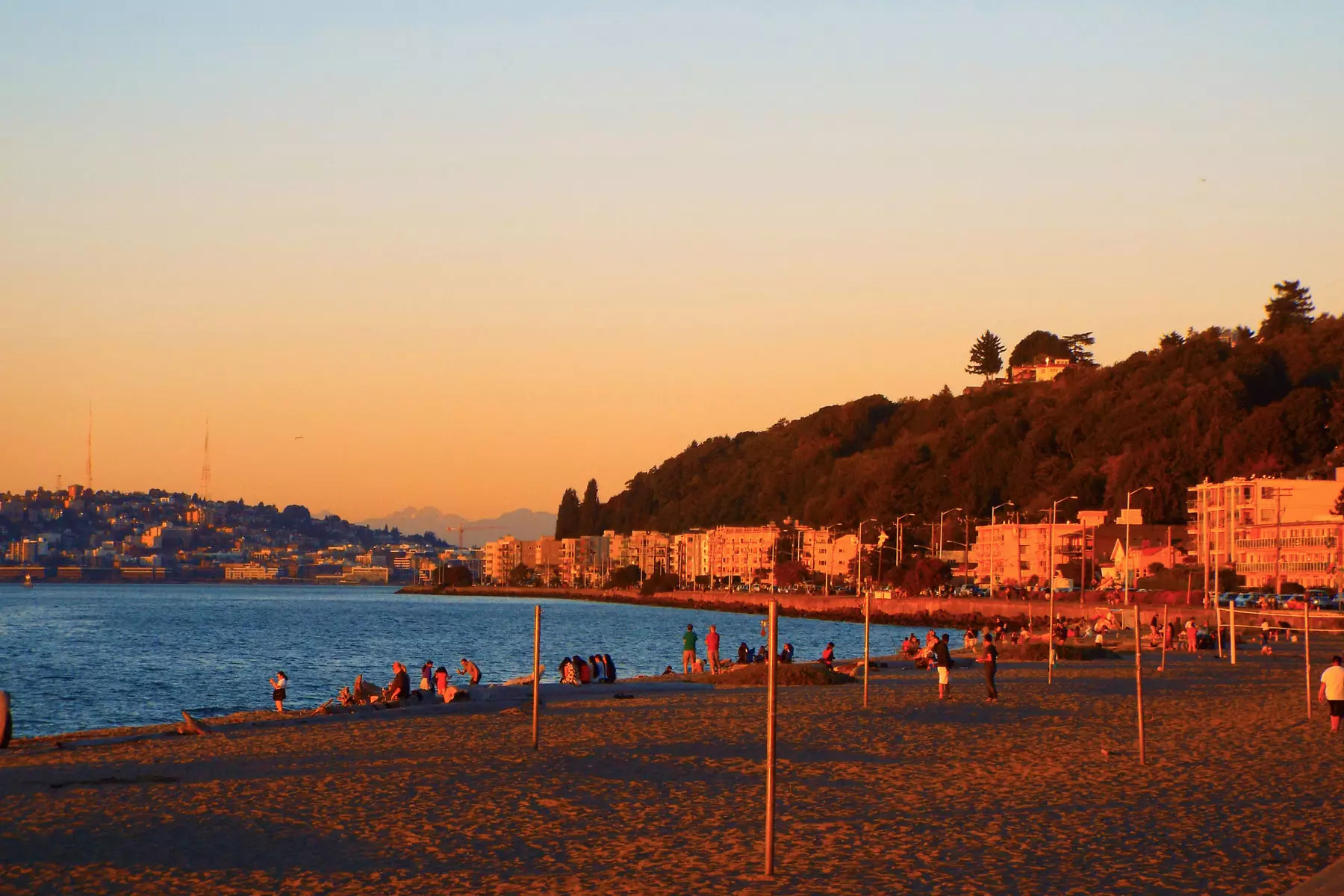 Alki beach sa panahon ng ginintuang oras sa Seattle na may mga taong nakapila sa beach na nanonood ng paglubog ng araw