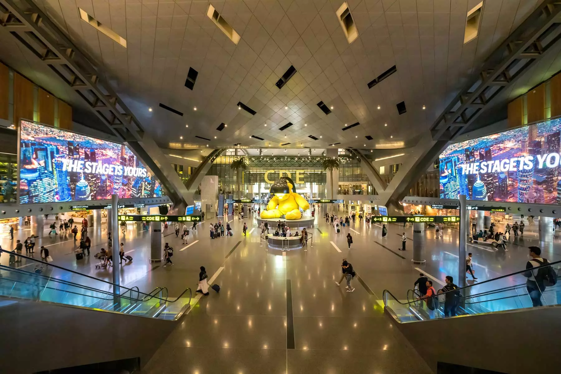 Mange turister er i Hamad International Airport Terminal med Big Yellow Bear Sculpture