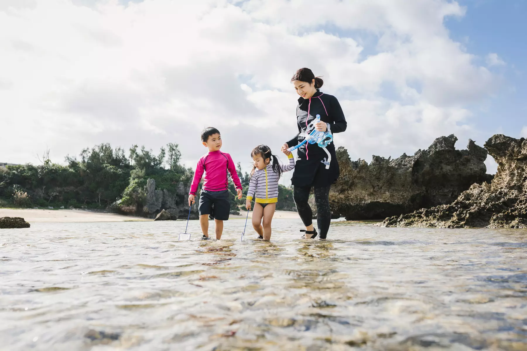 אמא, בן ובת אסיה משחקים בחוף הים באי אוקינאווה.