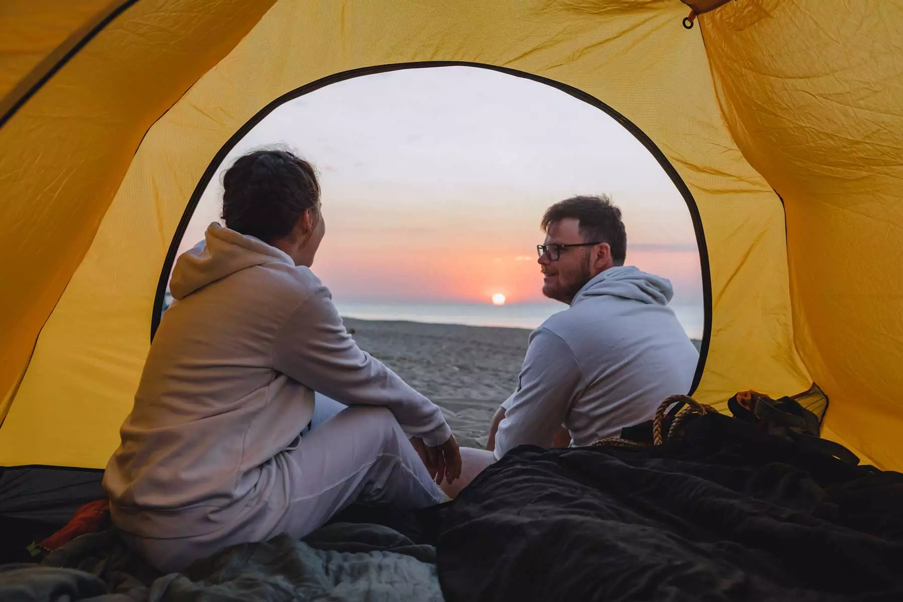 Un couple assis dans une tente de camping regardant le coucher du soleil.