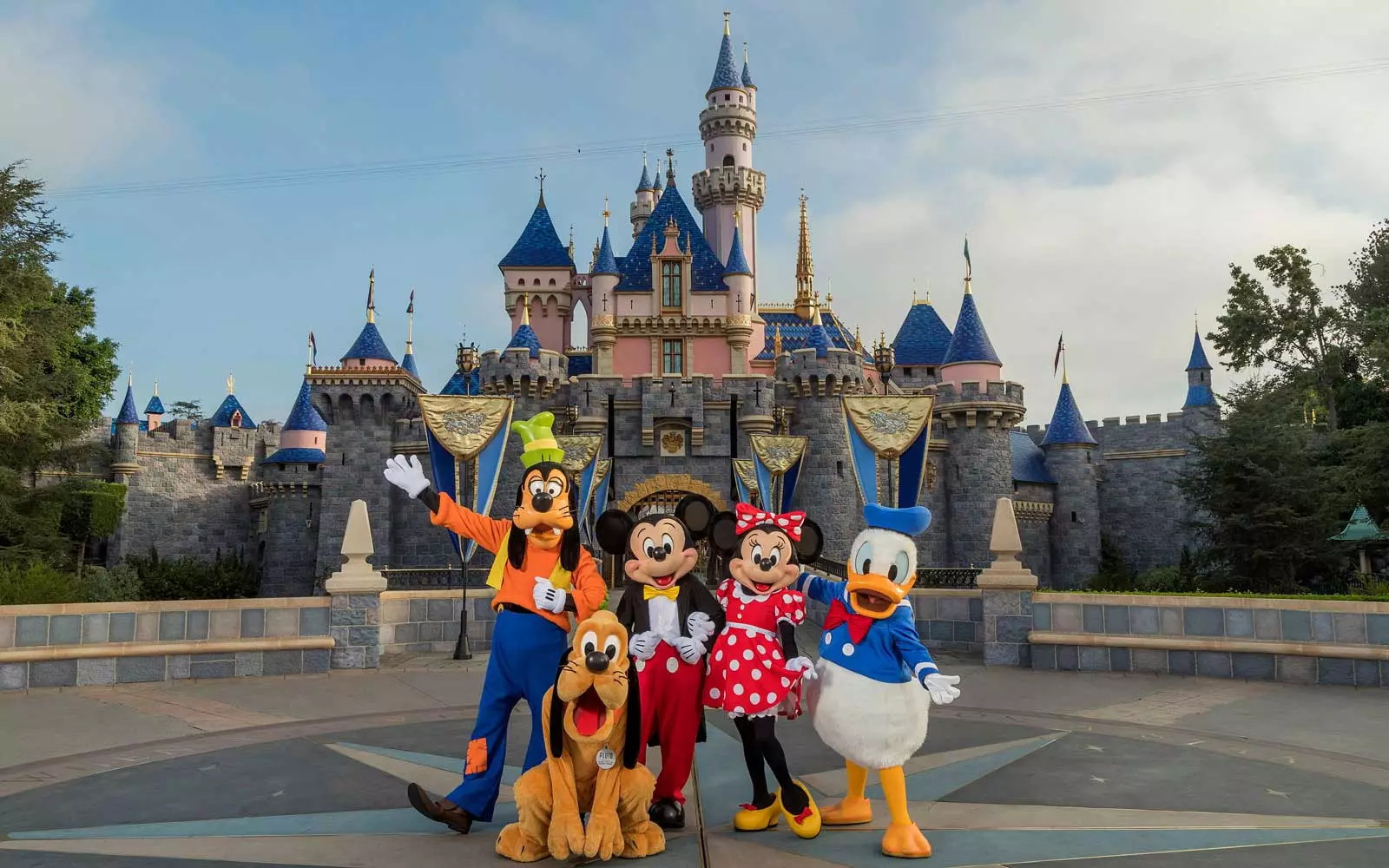 Personajele Disney, Goofy, Pluto, Mickey, Minnie și Donald Duck în fața castelului de la Disneyland din California
