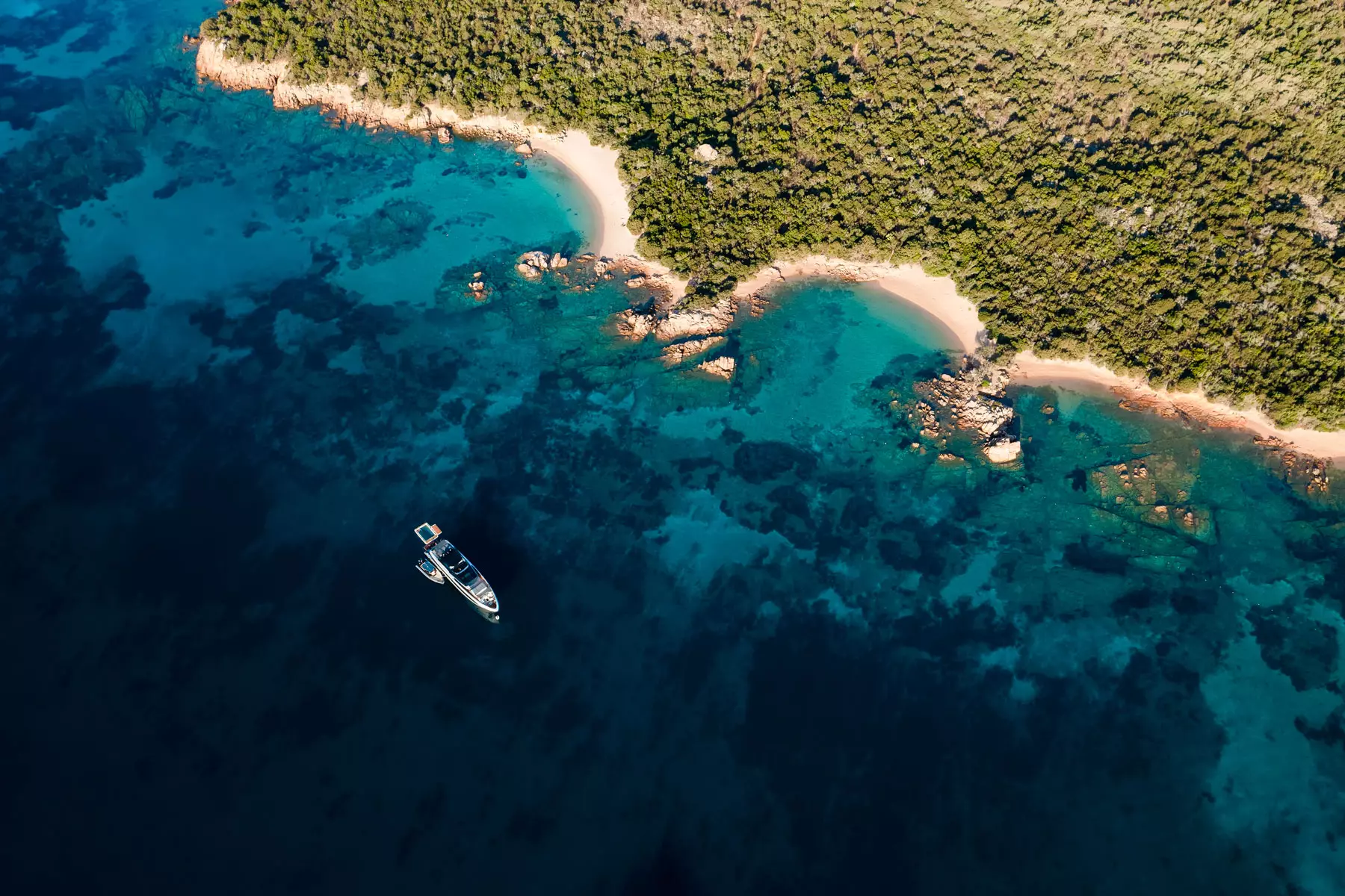 Bazı güzel plajları ve turkuaz bir su üzerinde yelken açan bir yat ile yeşil bir sahil şeridinin yukarıdan görünümü, çarpıcı havadan görünümü. Liscia Ruja, Costa Smeralda, Sardinya, İtalya.