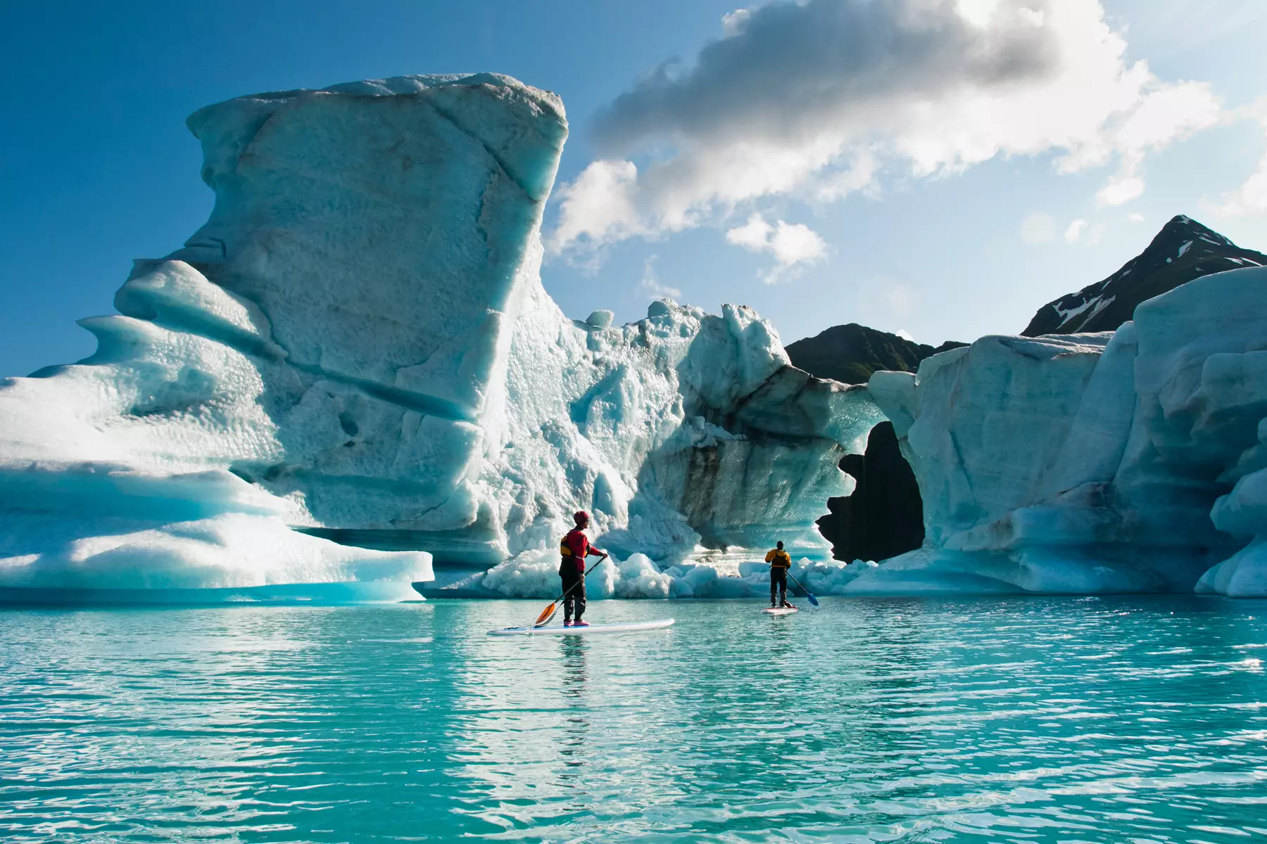 Dvije odrasle osobe na dasci za veslanje (SUP) promatraju otopljenu rupu u santi leda na medvjeđem jezeru u Nacionalnom parku Kenai Fjords na Aljasci.