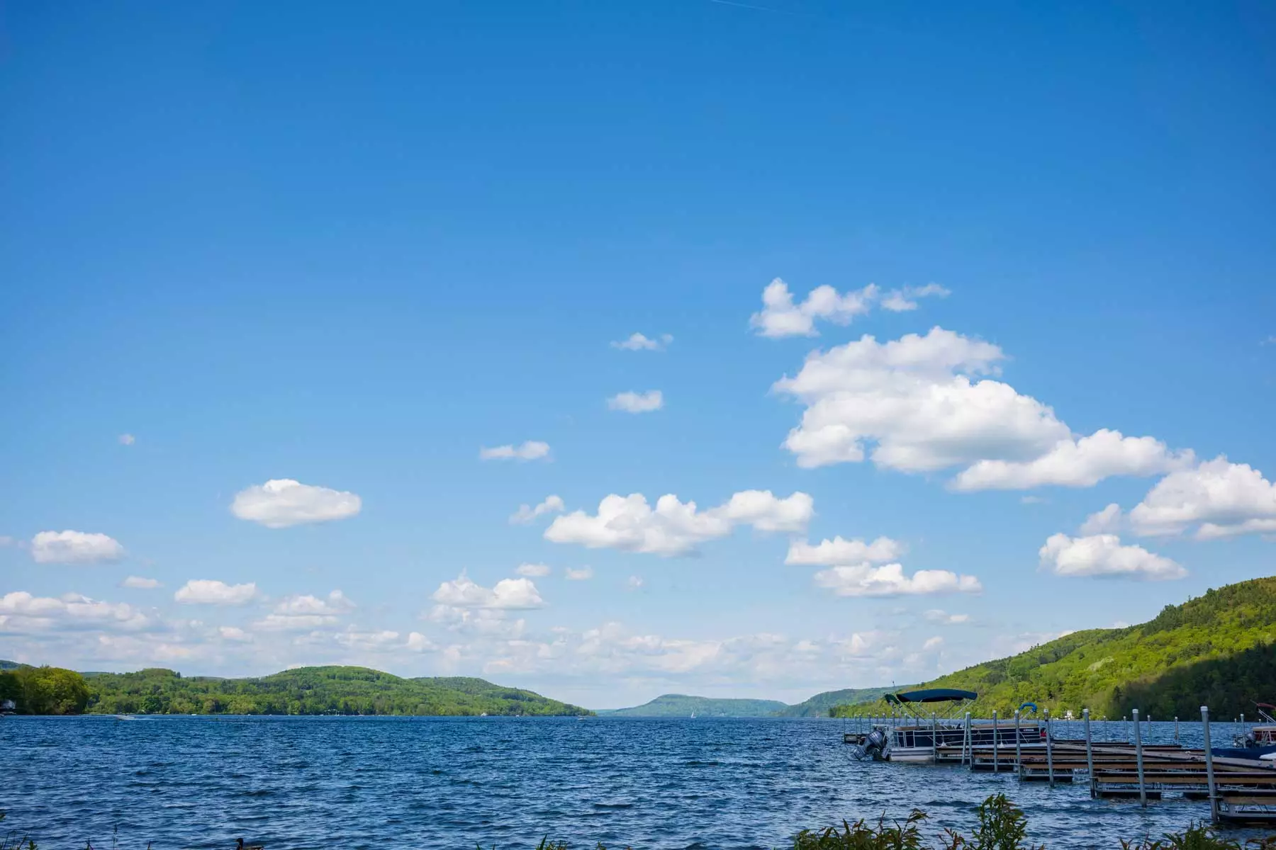 Maji ya buluu ya Ziwa la Otsego huko Cooperstown, New York, siku ya kiangazi yenye jua na mawingu angani, iliyopigwa picha karibu na kivuko.