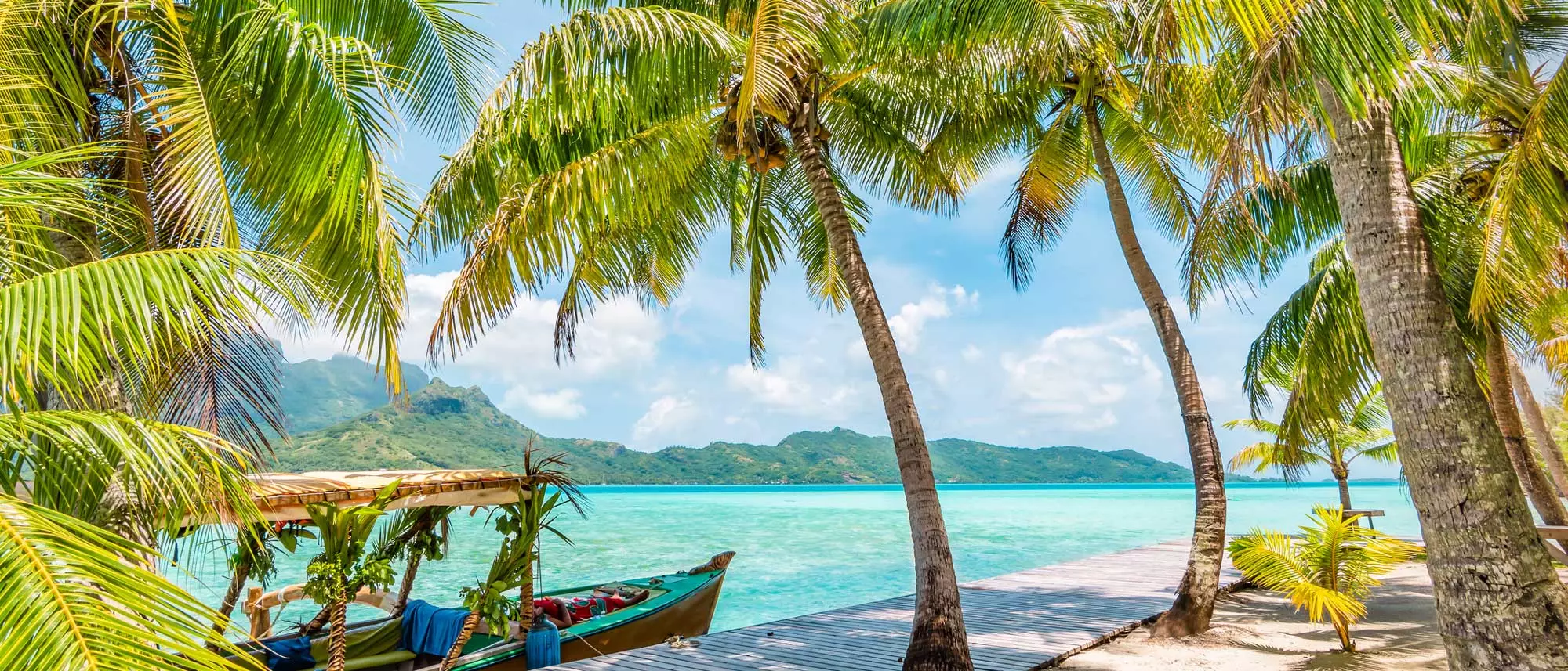 Bellissimo paesaggio estivo con palme da cocco sull'isola tropicale di Bora Bora, Polinesia francese. Barca turistica decorata ormeggiata alla banchina di legno.