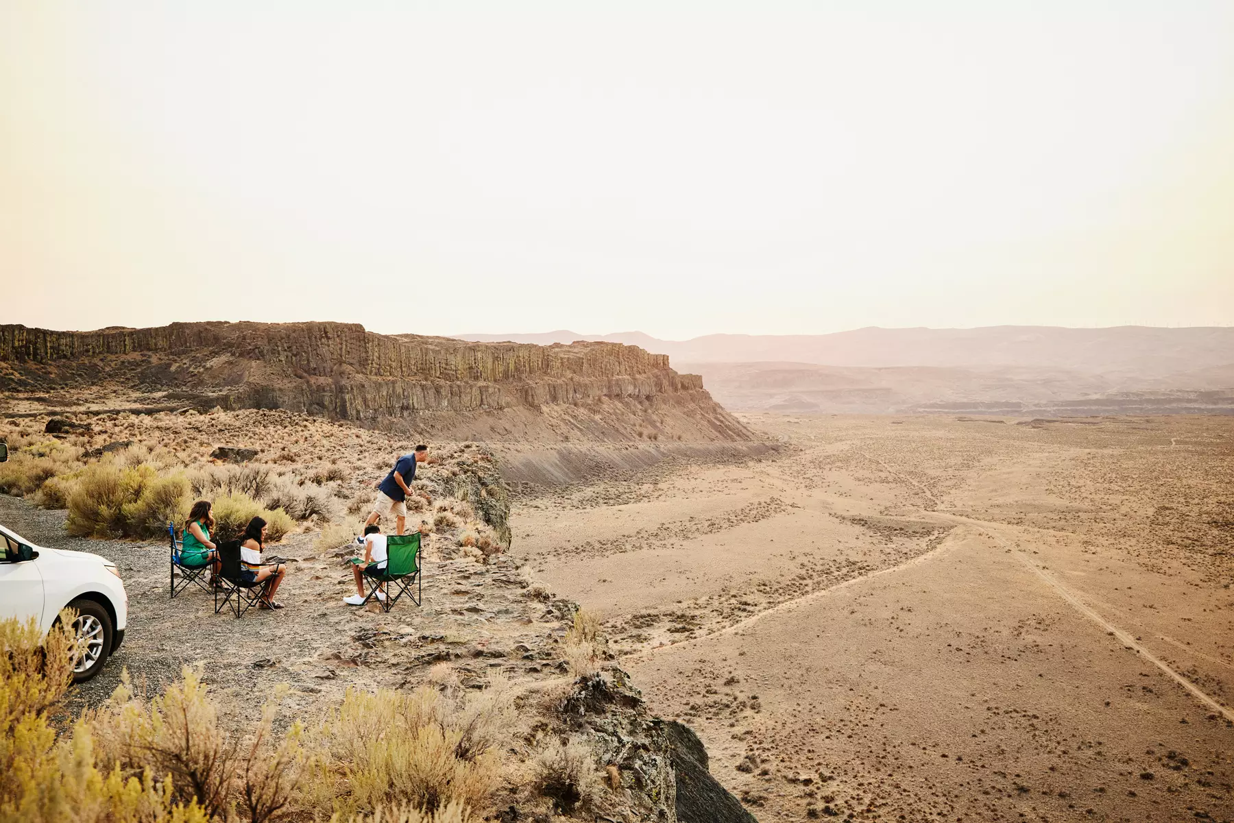 Famylje ûntspannen yn kampstoelen yn 'e buert fan desert canyon tidens simmer roadtrip