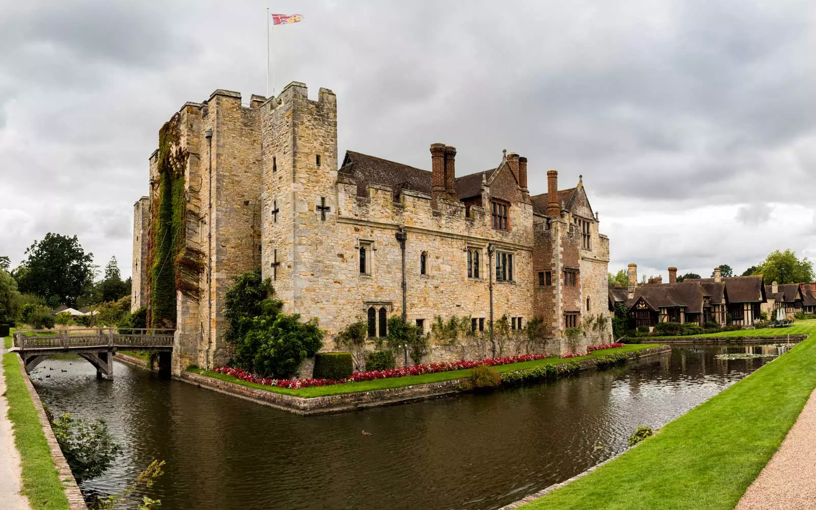 Uitsig op Hever-kasteel en sy grag op 'n bewolkte dag, met 'n vlag wat vol mas wapper