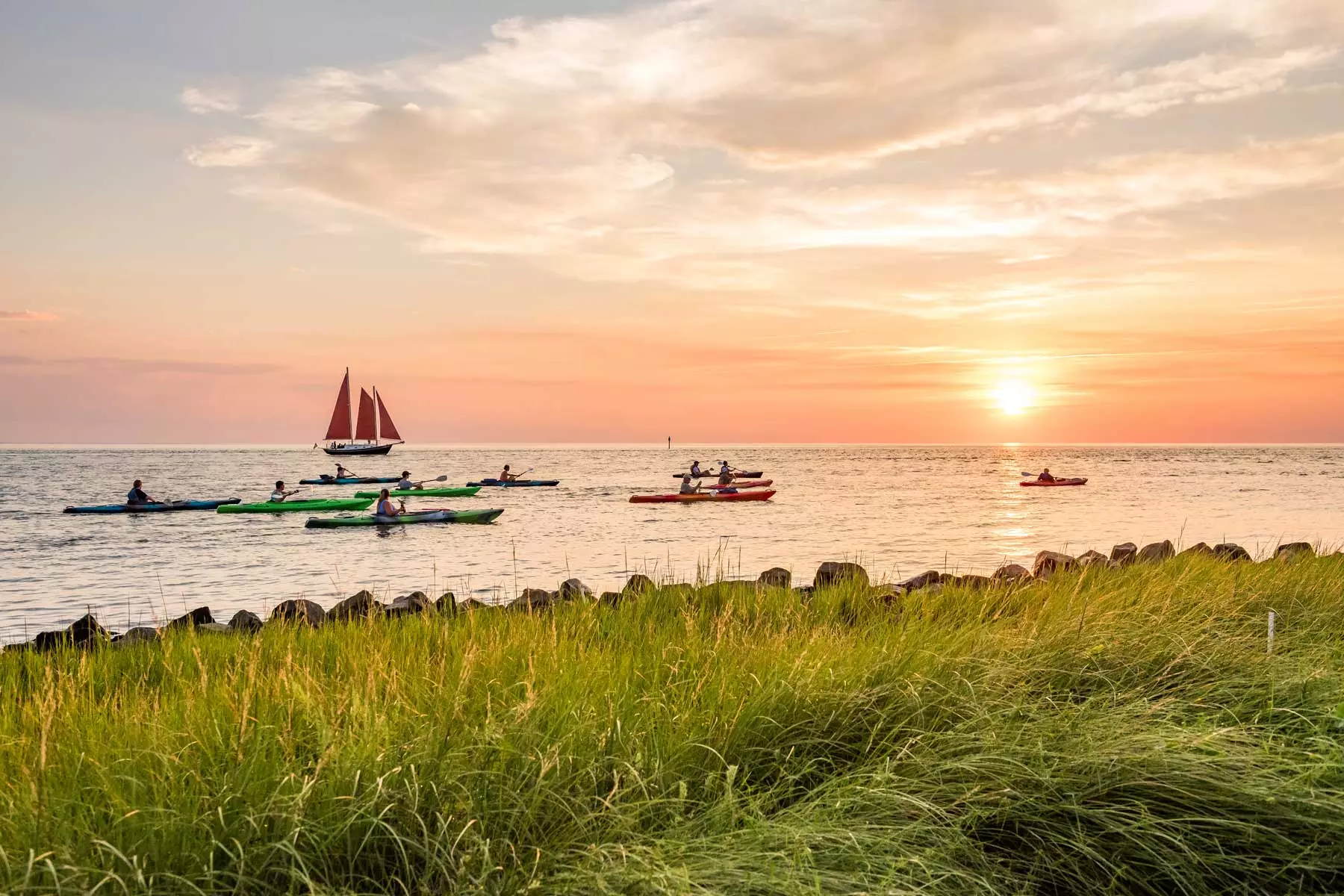 Kayakers da kwale-kwalen kwale-kwale a bakin teku a Pointer's Point a tsibirin Ocracoke a faɗuwar rana a lokacin bazara.