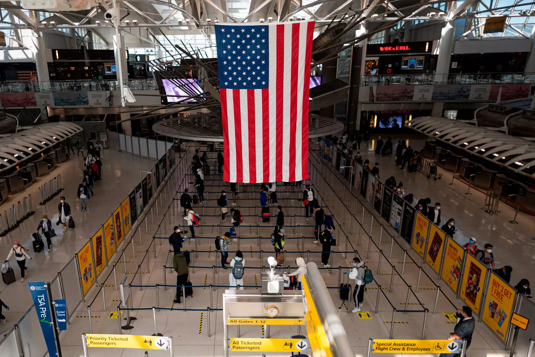 Passagéier, e puer Droen Masken a Schutzausrüstung, stinn an der Schlaang fir hire Fluch um Terminal 1 vum John F. Kennedy Fluchhafen (JFK) am Kader vun der neier Coronavirus Pandemie den 13. Mee 2020