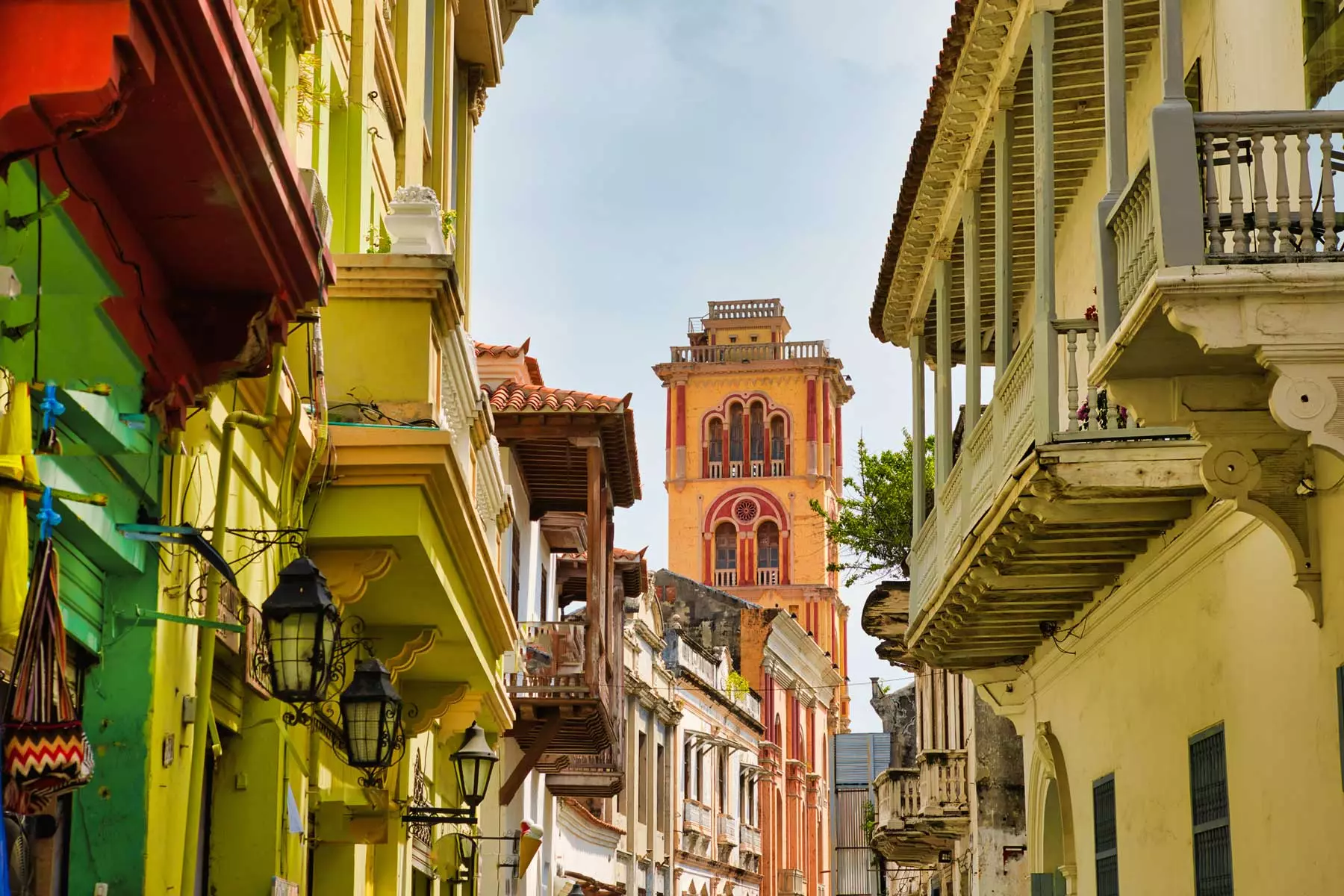 Casas coloniais espanholas em cores vivas e sortidas, alinhadas. Belos detalhes arquitetônicos são observados em todas as construções, além de charmosas varandas. Ao longe, uma torre robusta se destaca contra o céu azul suave.