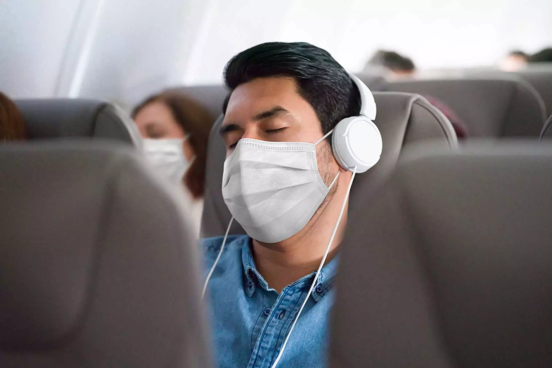 फ़ेसमास्क पहनकर हवाई जहाज़ पर यात्रा करता और सोता हुआ आदमी
