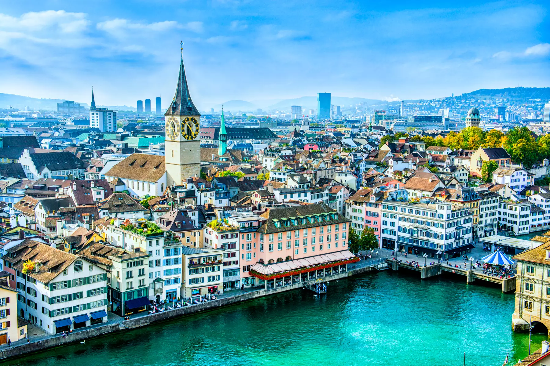 Aerial view sa Zurich, Switzerland. Gikuha gikan sa tore sa simbahan nga nag-umbaw sa Limmat River. Matahum nga asul nga kalangitan nga adunay dramatikong cloudscape sa ibabaw sa lungsod. Makita ang daghang tradisyonal nga Swiss nga mga balay, tulay ug simbahan.