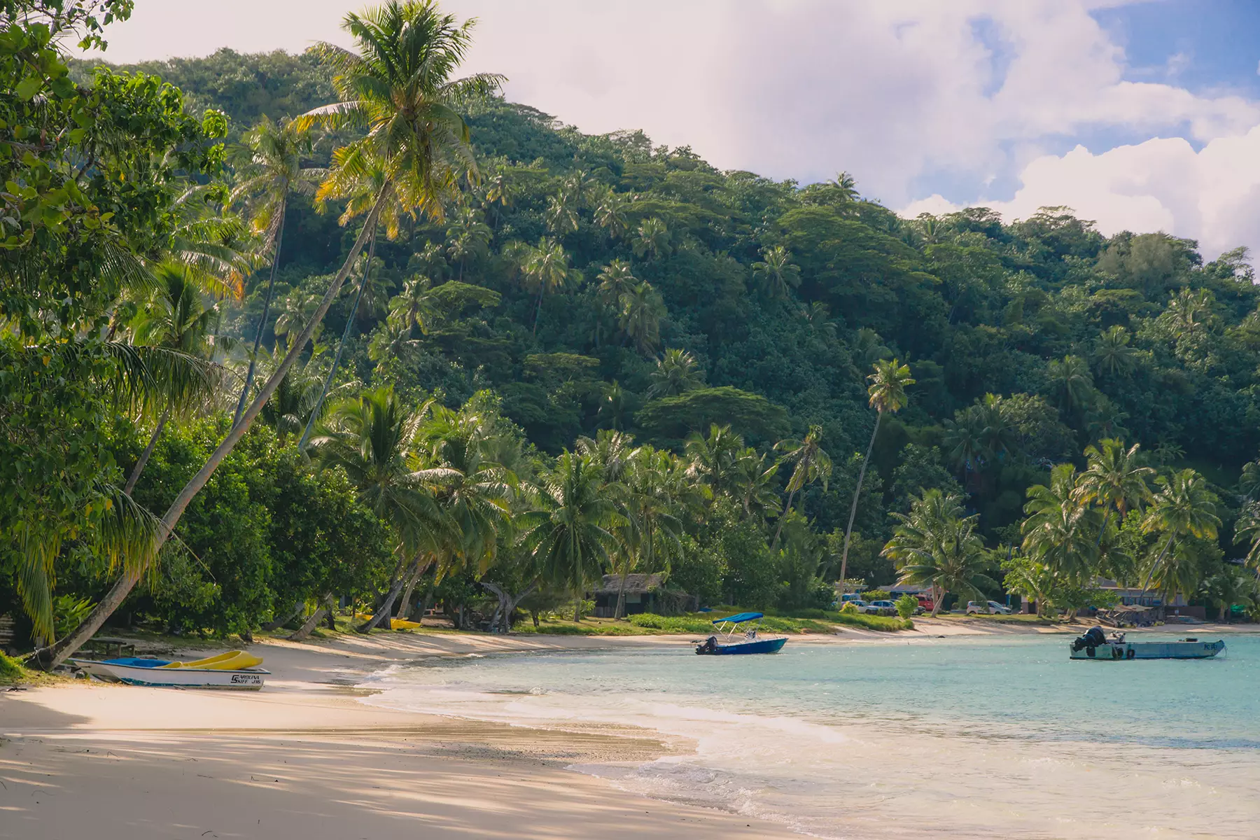 Matira Beach á Bora Bora á sólríkum degi með litlum bátum og kókoshnetupálmatrjám.