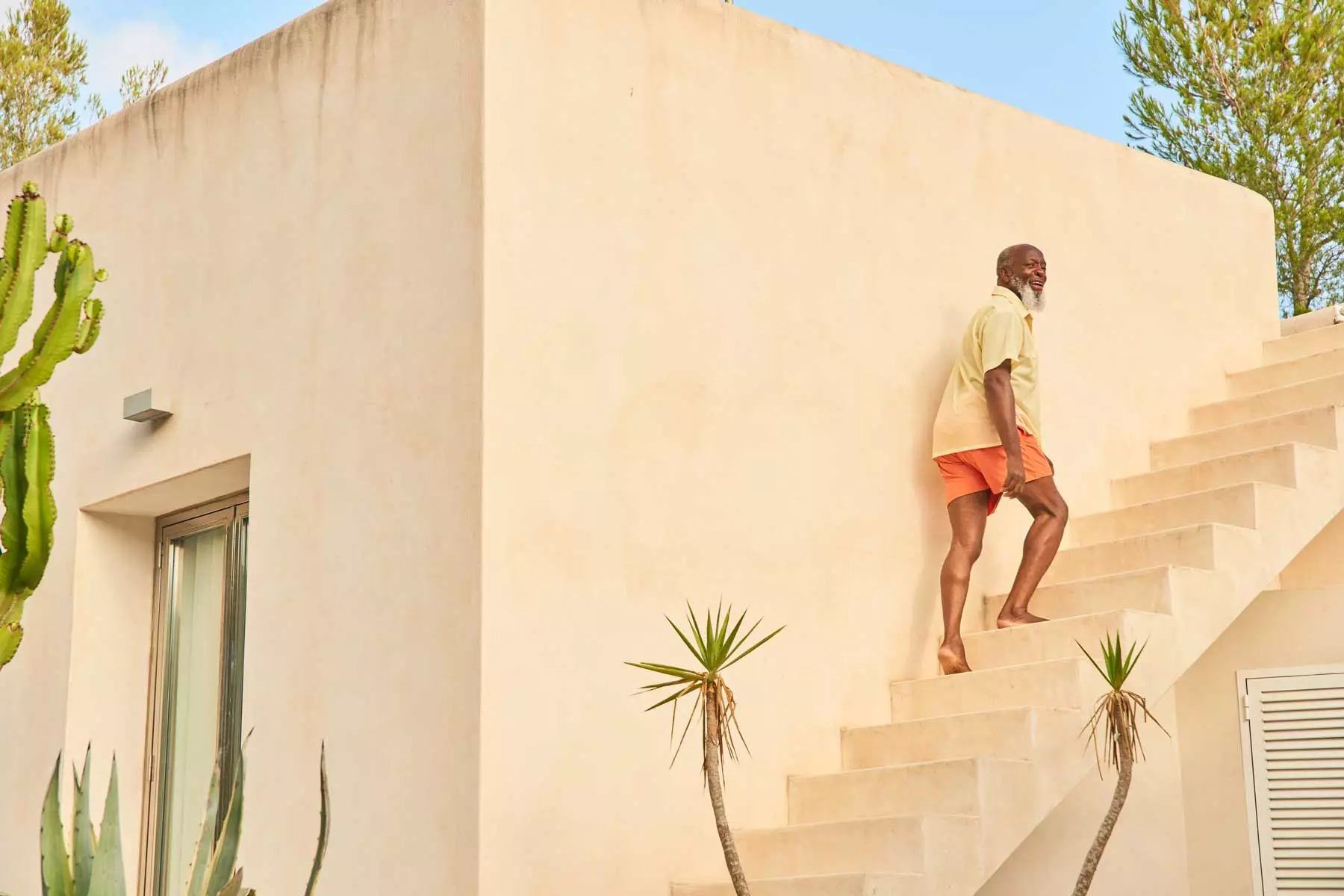 Un uomo con una maglietta gialla e pantaloncini arancioni sale le scale fino a una terrazza sul tetto mentre è in vacanza