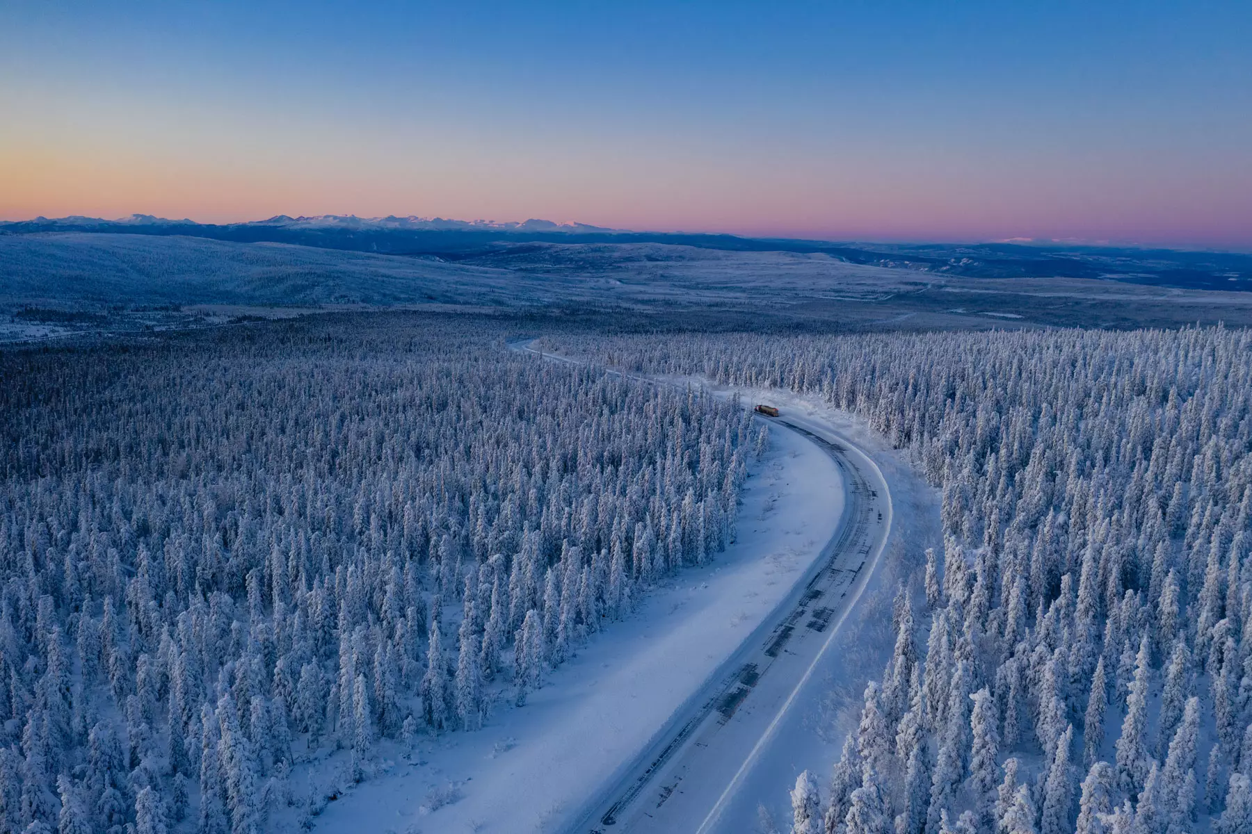 Pemandangan saka udara nalika srengenge surup saka lanskap musim dingin sing amba saka wit pinus sing ditutupi salju ing Dalton Highway ing Alaska