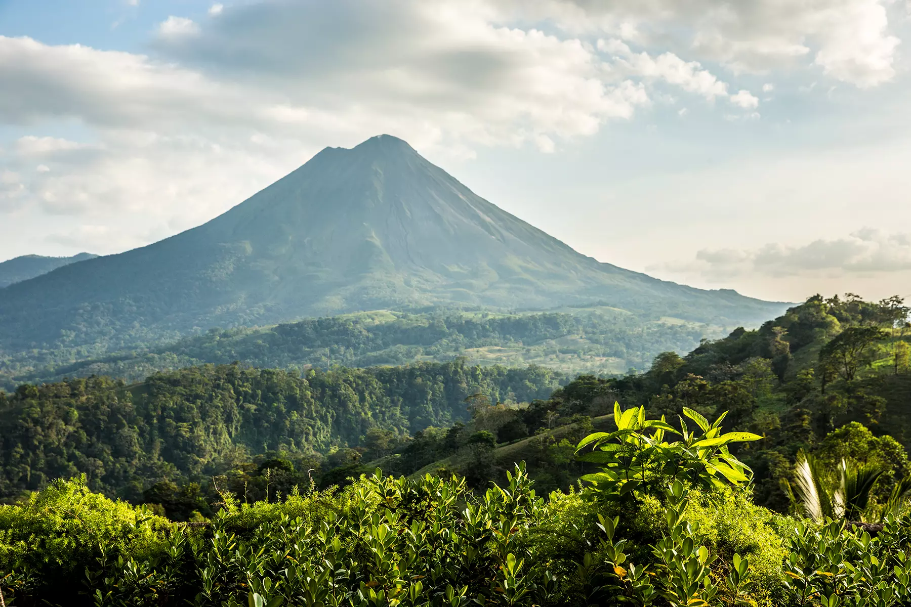 Bidikan lanskap Gunung Api Arenal di Kosta Rika dengan vegetasi subur di latar depan