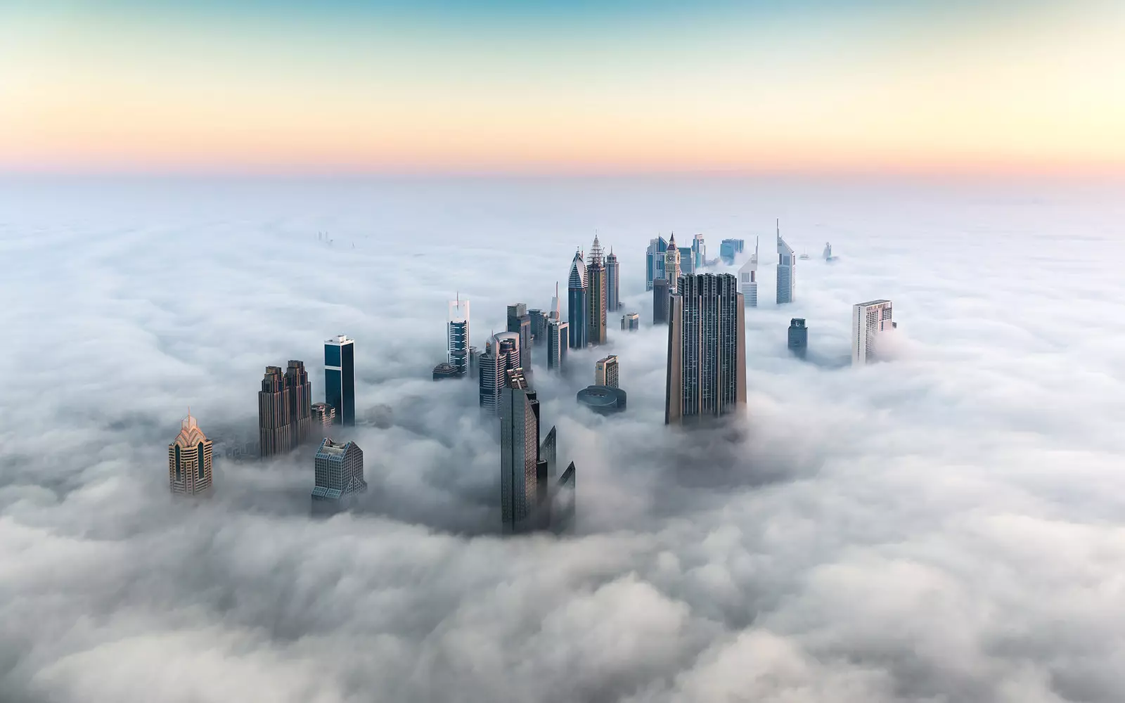 Letecký pohľad na Dubaj s vežou Index Tower, Emirates Towes a panorámou Sheikh Zayed Road v hustej hmle pred červeným východom slnka a modrou oblohou. Dubaj, Spojené arabské emiráty