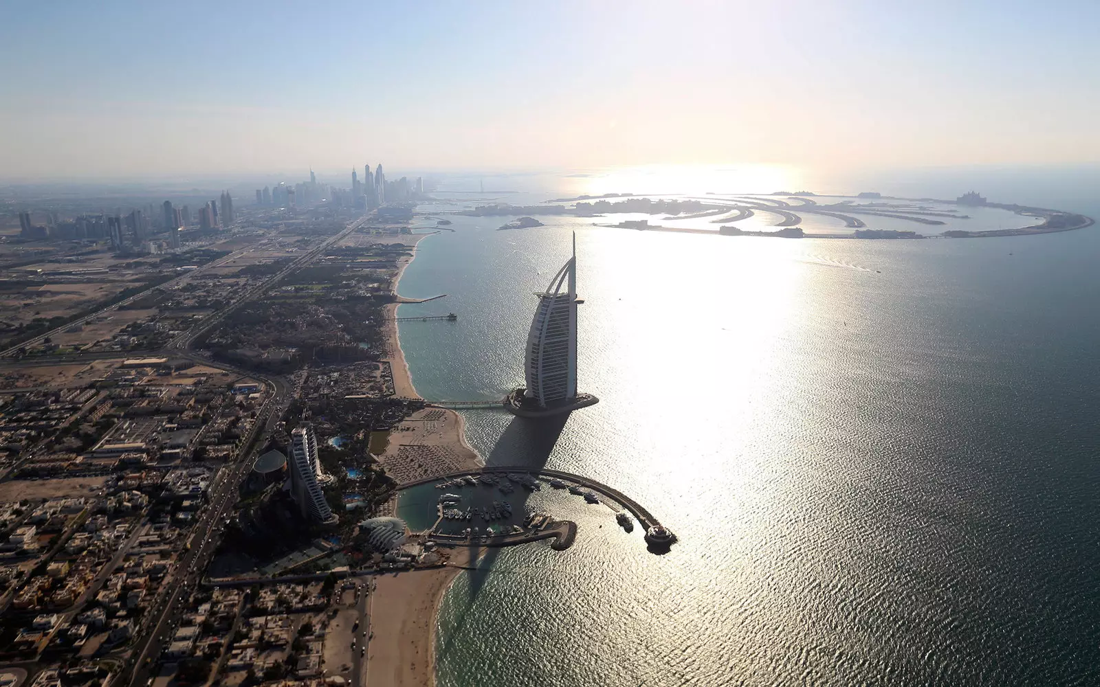 Mestské mrakodrapy stoja na panoráme za luxusným hotelom Burj Al Arab v strede, hotelom Jumeirah Beach, vľavo v strede, a súostrovím Jumeirah Palm vpravo hore na pobreží Dubaja v Spojených arabských emirátoch v utorok 11. novembra 2014 Klesajúci kurz