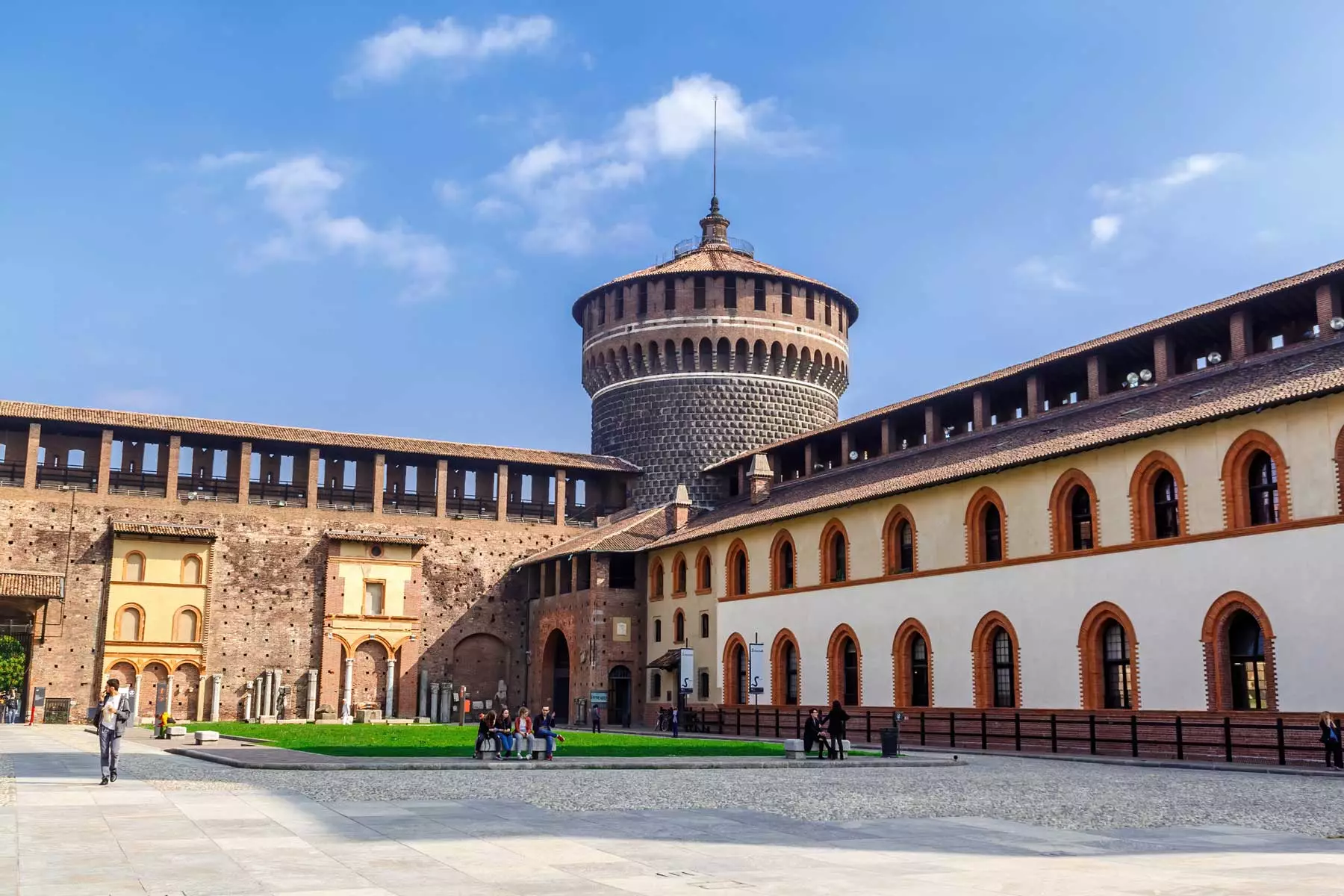 Starý středověký hrad Sforza Castello Sforzesco, zelený trávník nádvoří, modrá obloha bílé mraky pozadí.