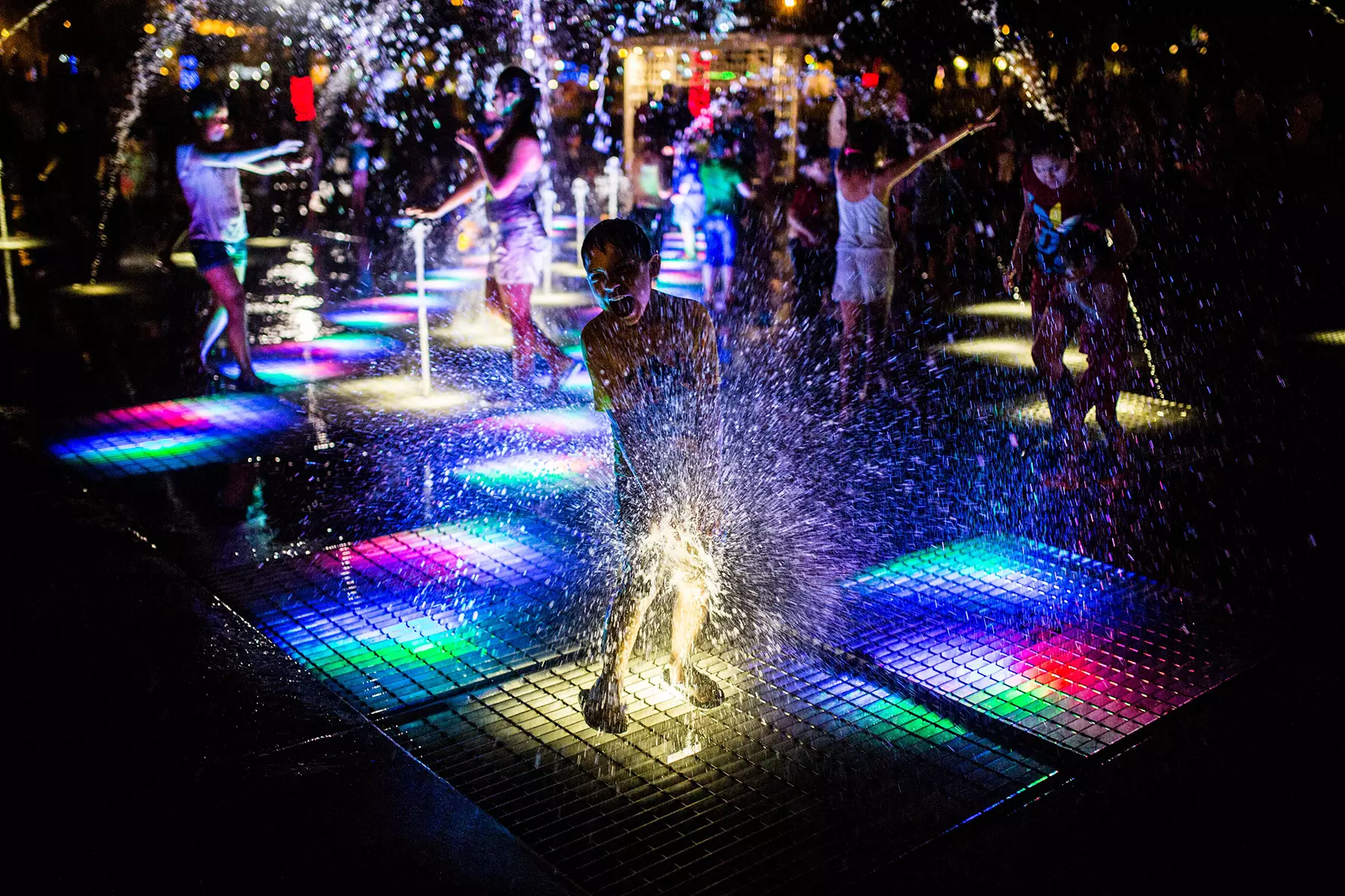 La gente juega en una fuente iluminada en el Circuito Mágico del Agua