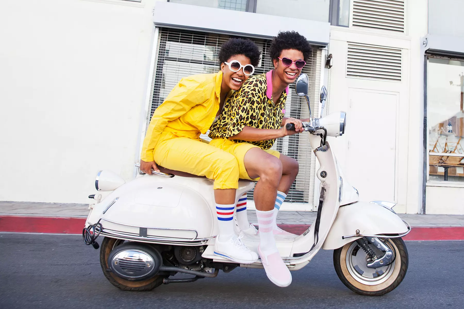 Un jeune couple branché portant des tenues jaunes et de grandes lunettes de soleil sur un scooter dans une rue de la ville regardant la caméra en souriant