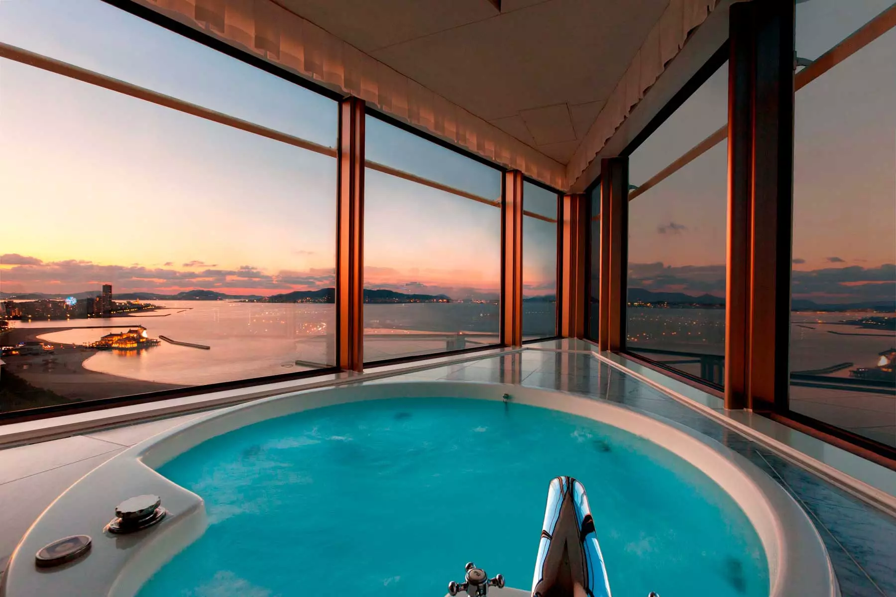 อ่างน้ำร้อนส่วนตัวในร่มของ Hilton Fukuoka Sea Hawk พร้อมทิวทัศน์ของท่าเรือในเวลากลางคืน