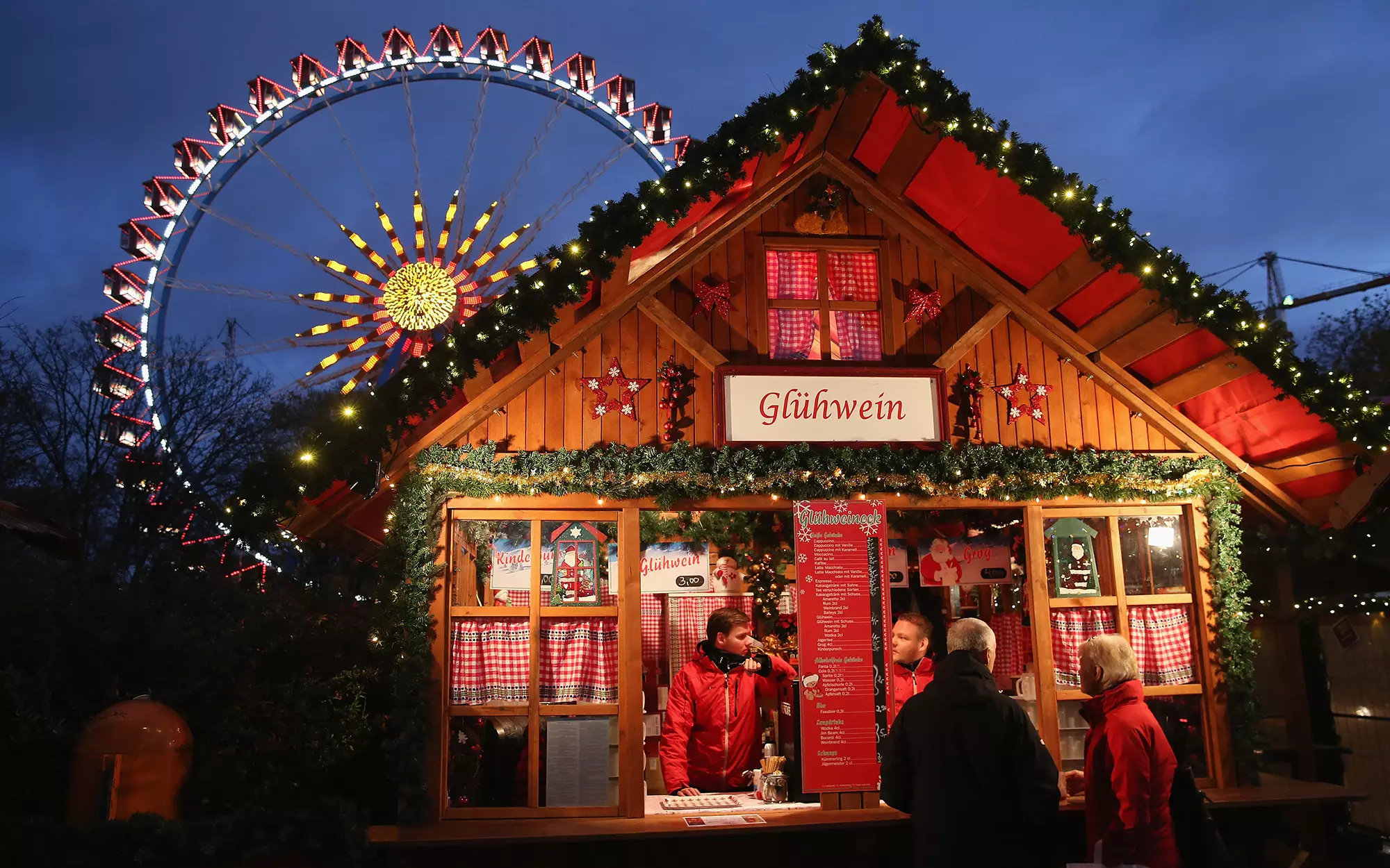 BERLIN, NEMČIJA - 24. NOVEMBER: Obiskovalci se ustavijo na stojnici, kjer prodajajo Gluehwein, poleg osvetljenega panoramskega kolesa na božičnem trgu na Alexanderplatzu na dan odprtja tržnice 24. novembra 2014 v Berlinu v Nemčiji. Božični trgi po Nemčiji