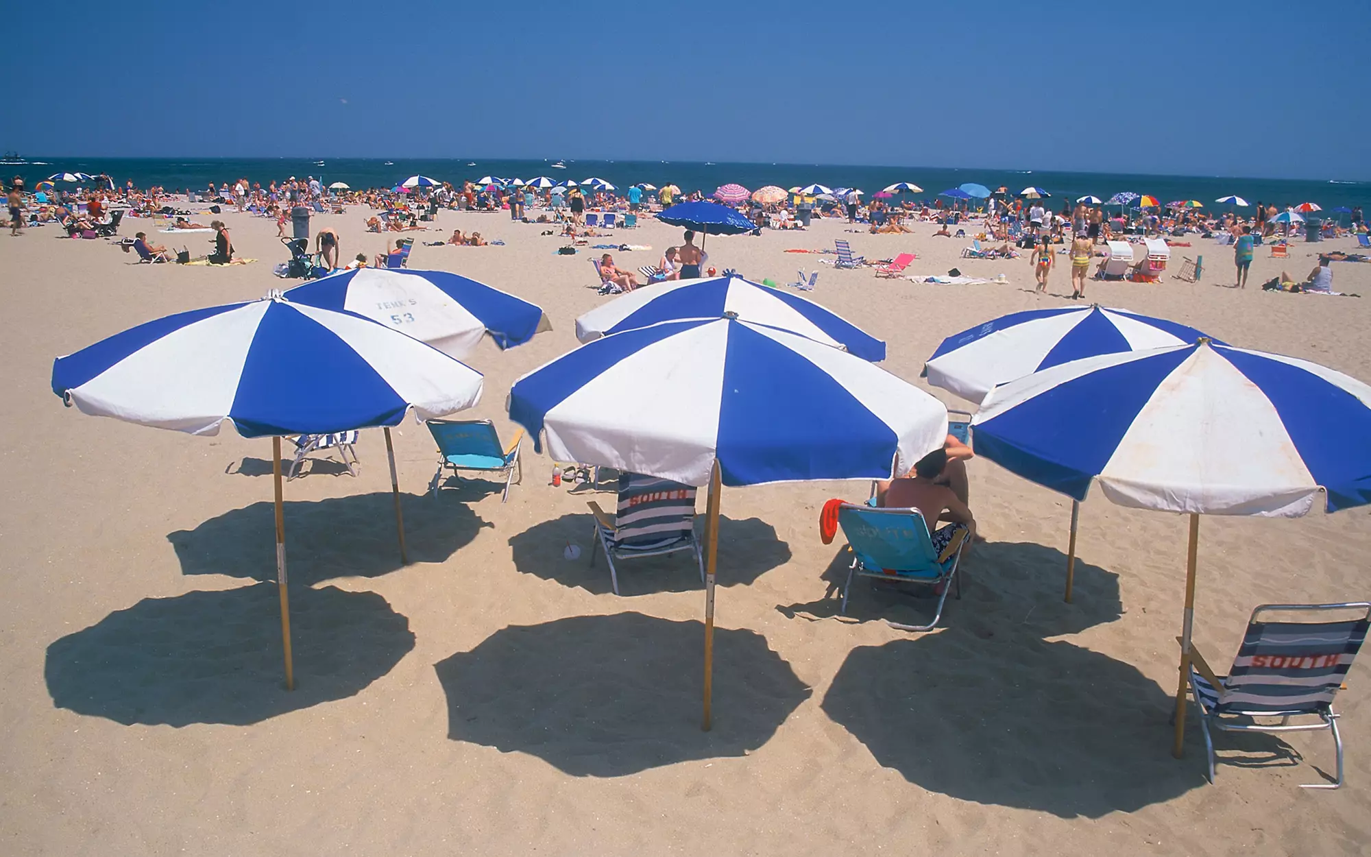 Abantu abanezambulela ezishisa ilanga ogwini olunesihlabathi esimhlophe, i-Atlantic Ocean, i-Point Pleasant, i-NJ