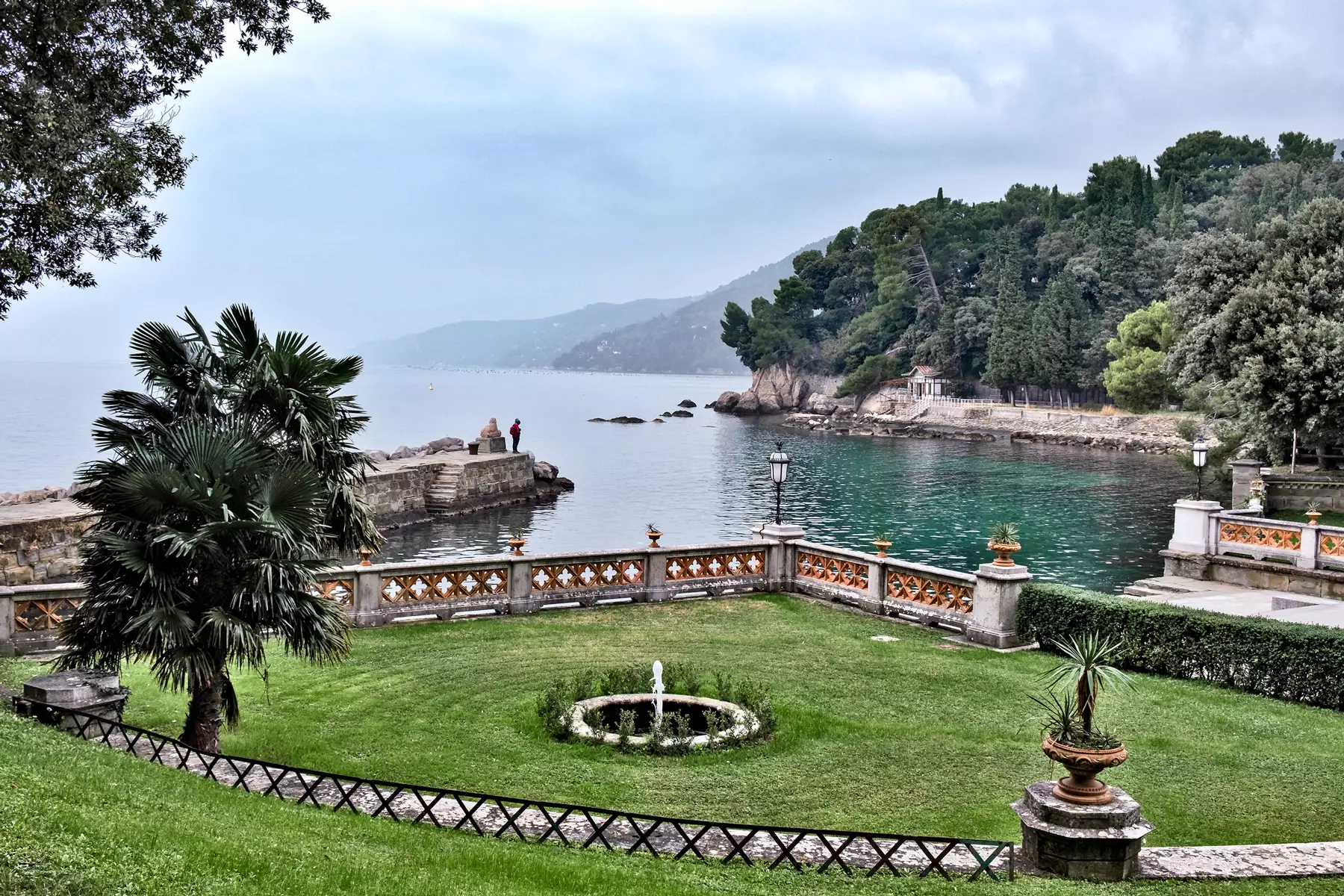 Vedere a unei grădini dintr-un parc public și a golfului Trieste învecinată cu castelul Miramare din Trieste, Italia.