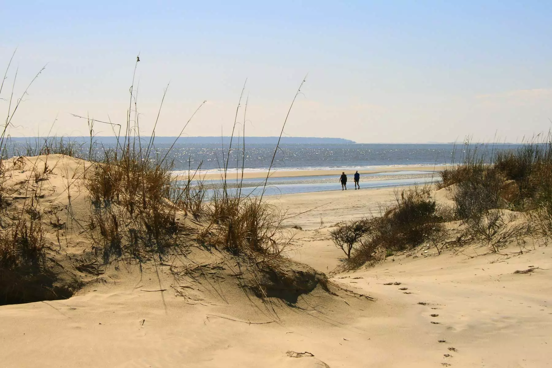 Sjoch troch de dunen nei twa minsken dy't op it strân rinne by Jekyll Island, Georgia