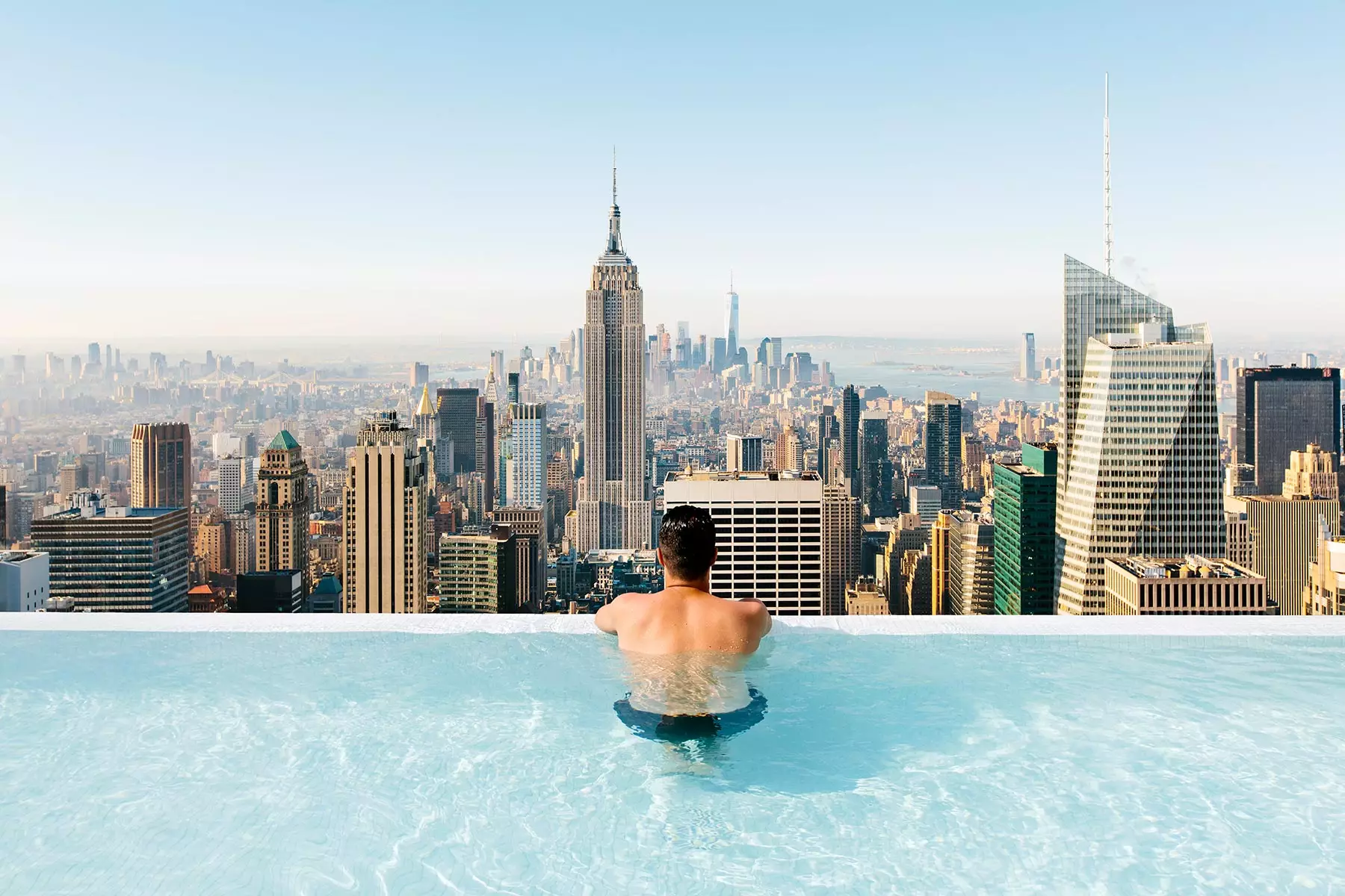 Un hombre relajándose en una piscina con vistas al horizonte de la ciudad de Nueva York