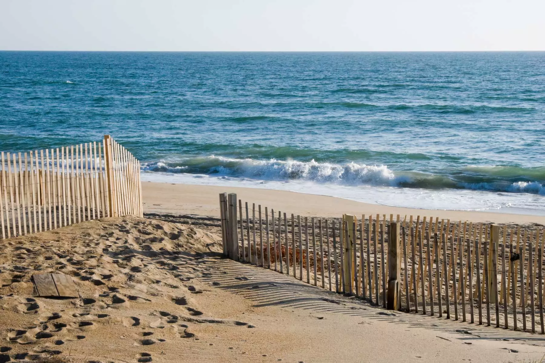 Ombak pecah ing pantai ing wayah esuk kanthi pager kontrol erosi ing gumuk pasir, Outer Banks ing Nags Head, North Carolina