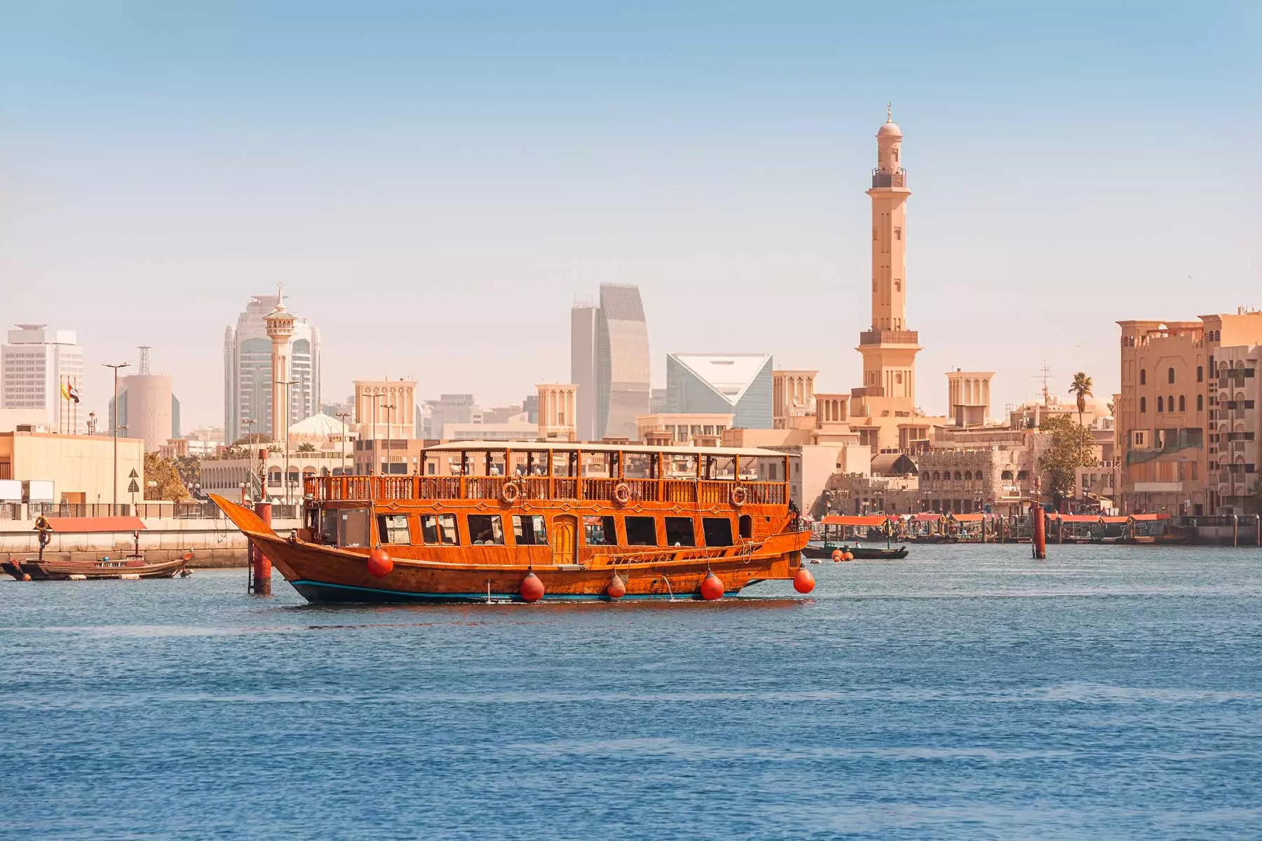 Un autèntic creuer de fusta navega i transporta turistes pel canal Dubai Creek amb gratacels i minarets de mesquites al fons. Viatges i visites turístiques