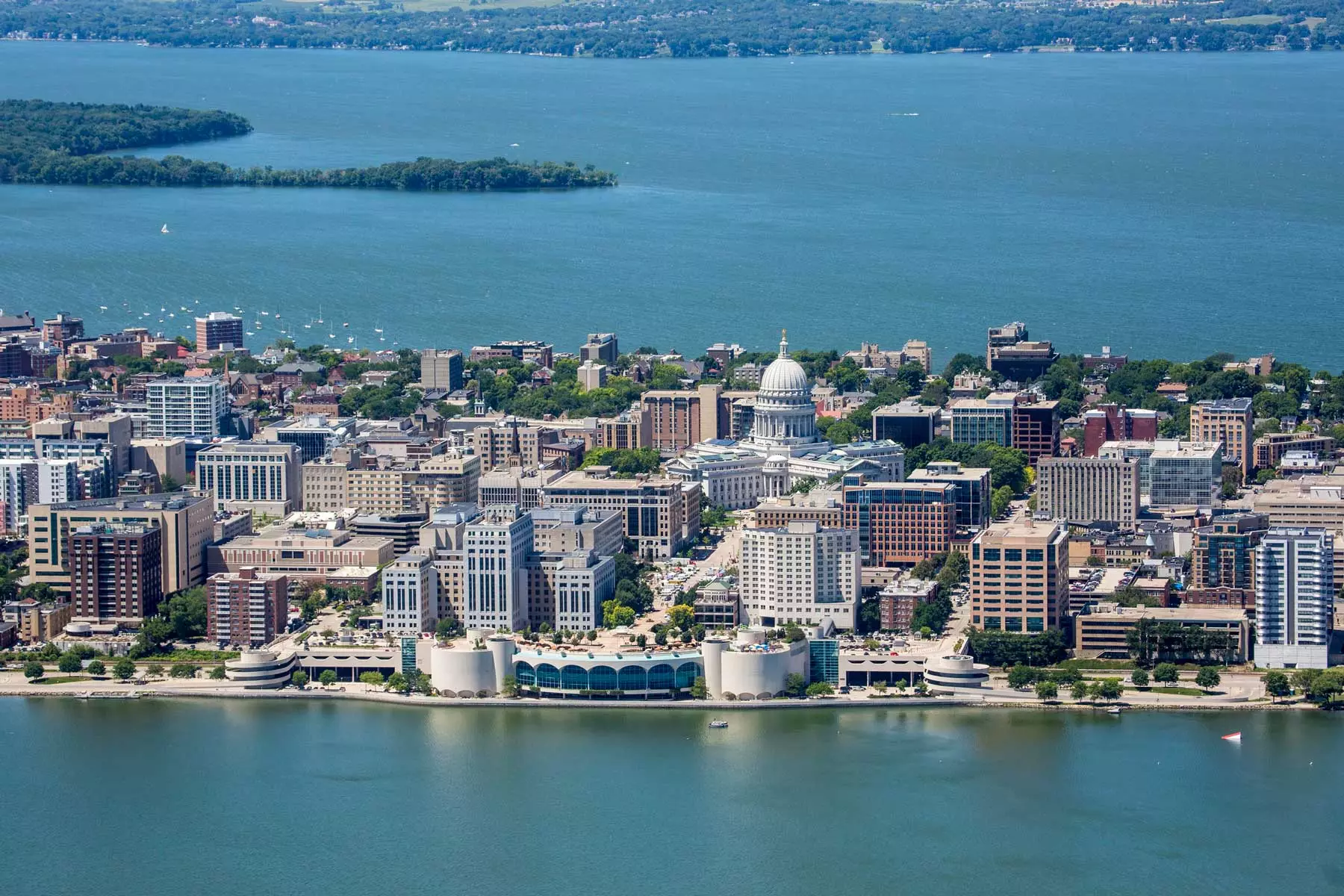 Eine Luftaufnahme des Streifens von Madison Wisconsins Innenstadt, die sowohl die Gebäude Monona Terrace und Capitol als auch Picnic Point im Hintergrund zeigt. Zeigt auch Teile der beiden Seen Monona und Mendota.