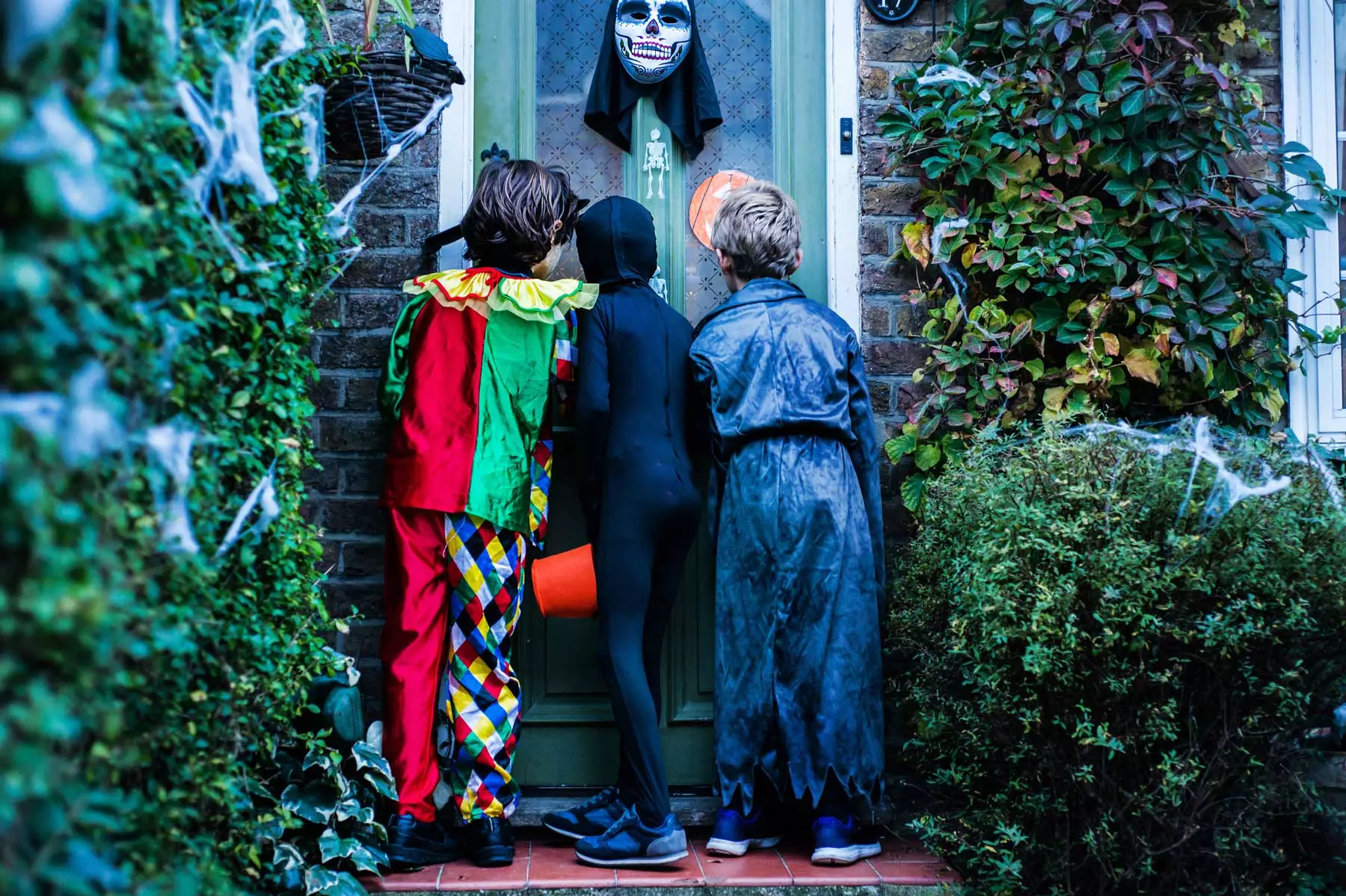 Três garotos em trajes de halloween, em pé na porta, gostosuras ou travessuras, vista traseira